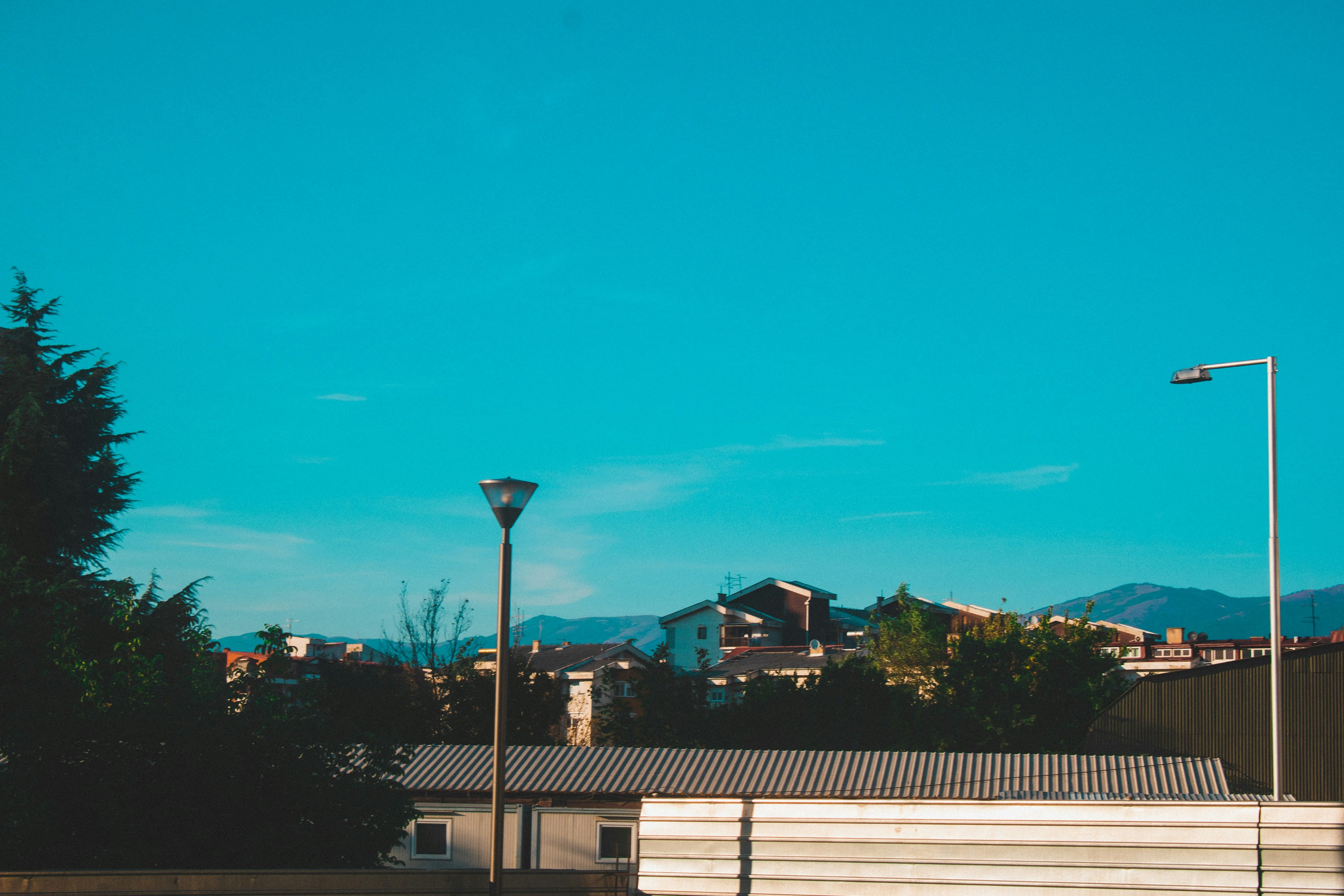 Street scene with a lamppost, tree, and old houses behind an aluminum fence under a clear blue sky.