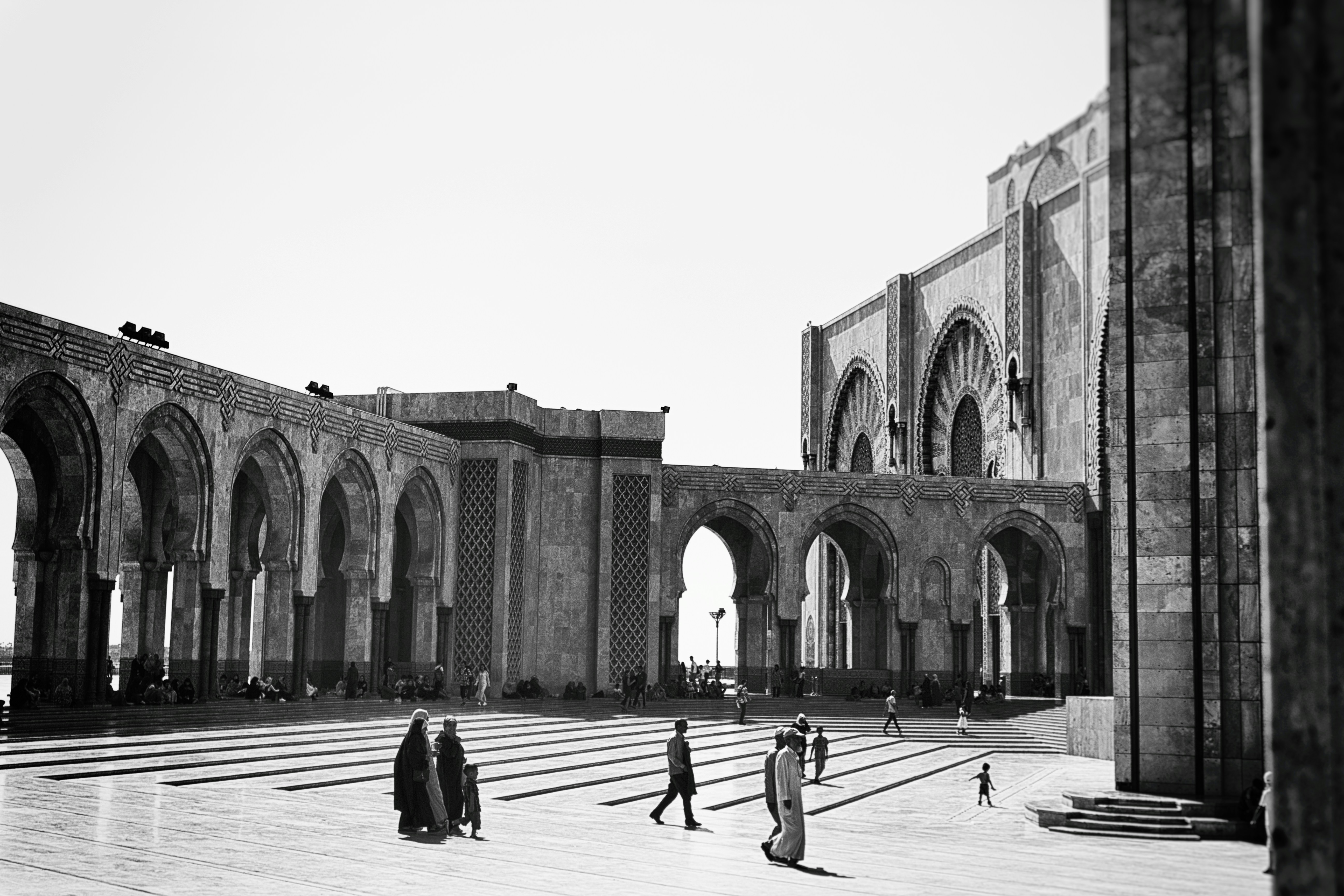 Black and white view of people walking through arches of a grand architectural structure.