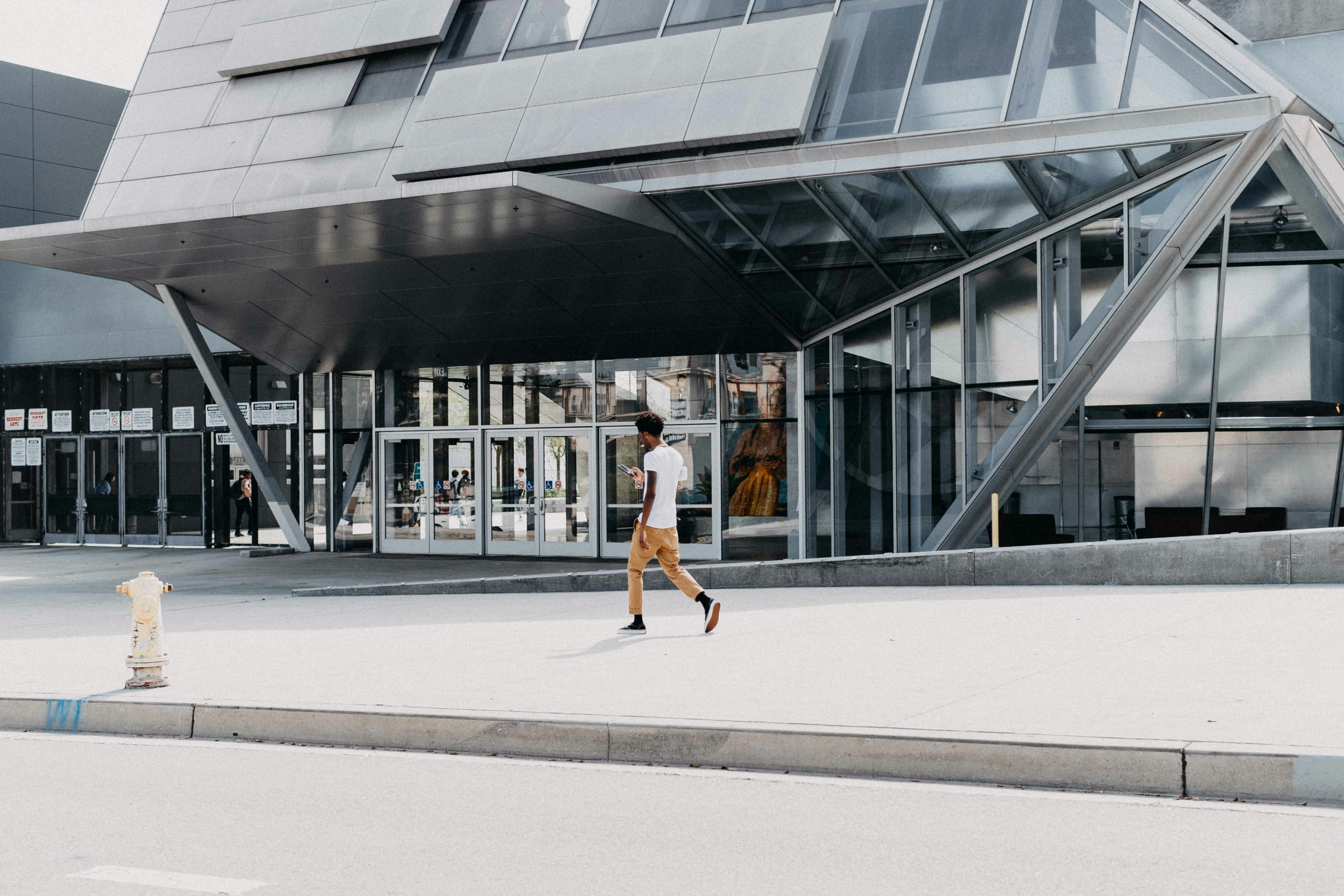 Glass-Canopy Crossing: A solitary pedestrian threads the modern entrance