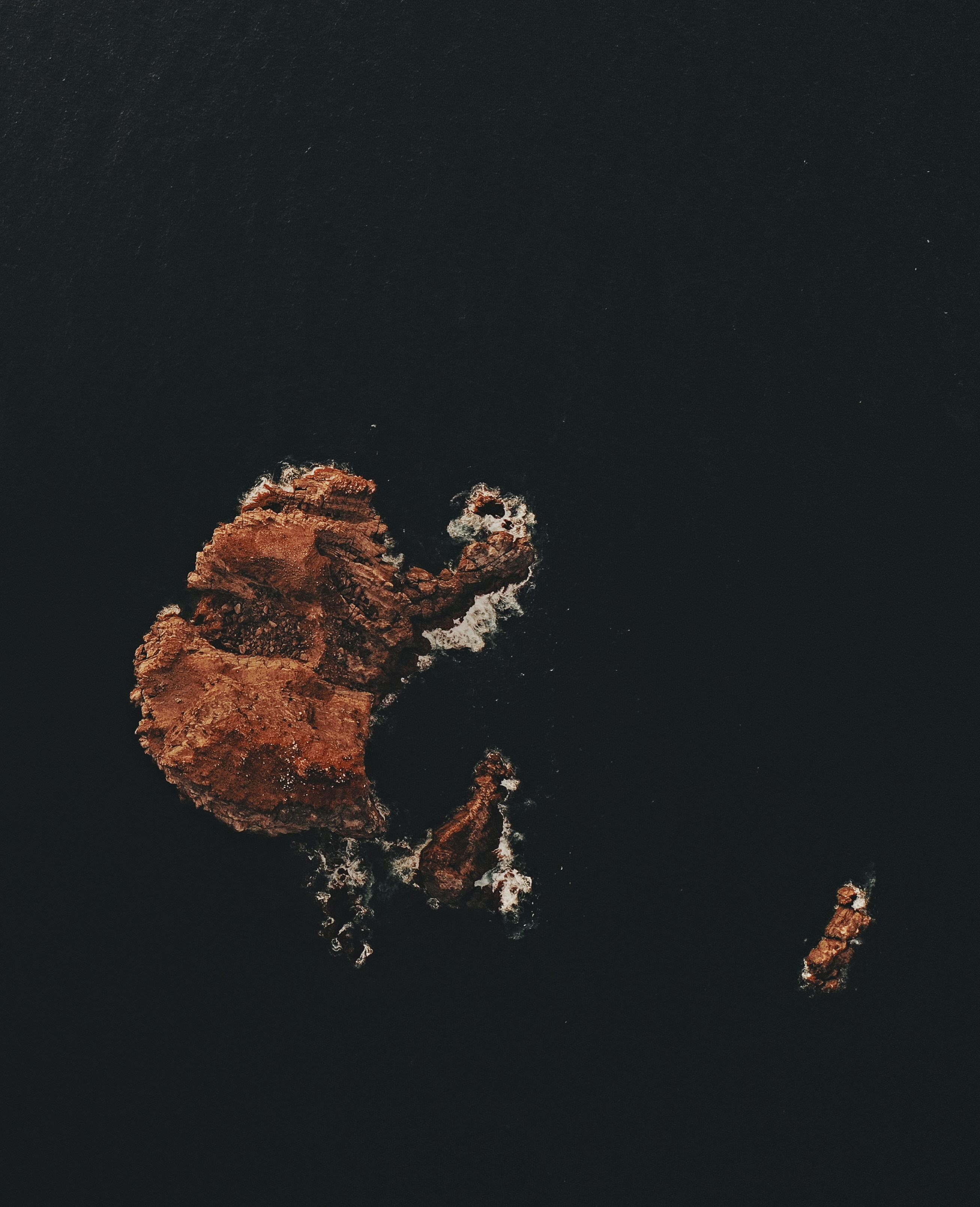Aerial view of a rugged island surrounded by dark waters, showcasing its unique geological features and textures.