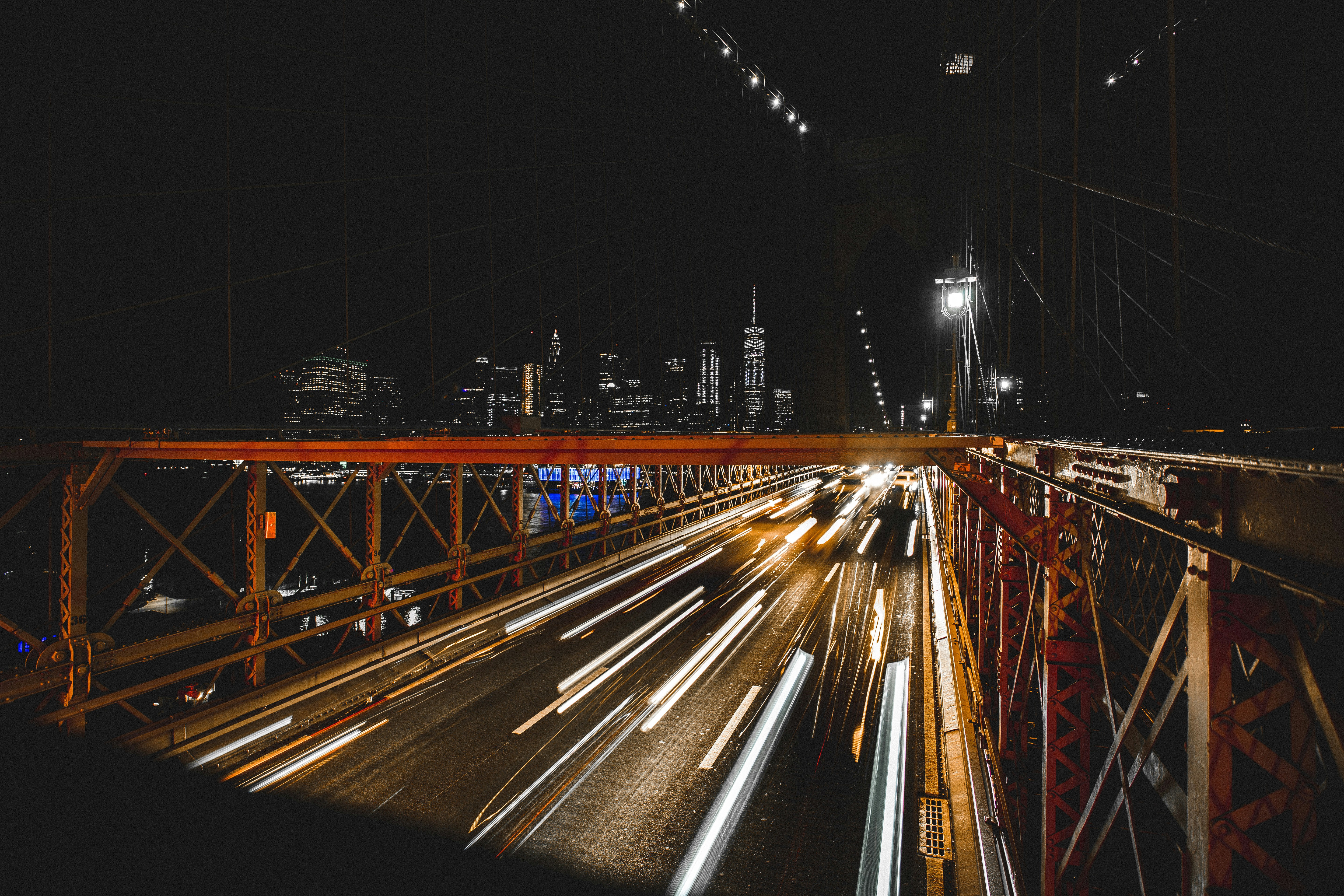 Dynamic light trails from vehicles on a bridge against a city skyline at night, showcasing urban life and movement.
