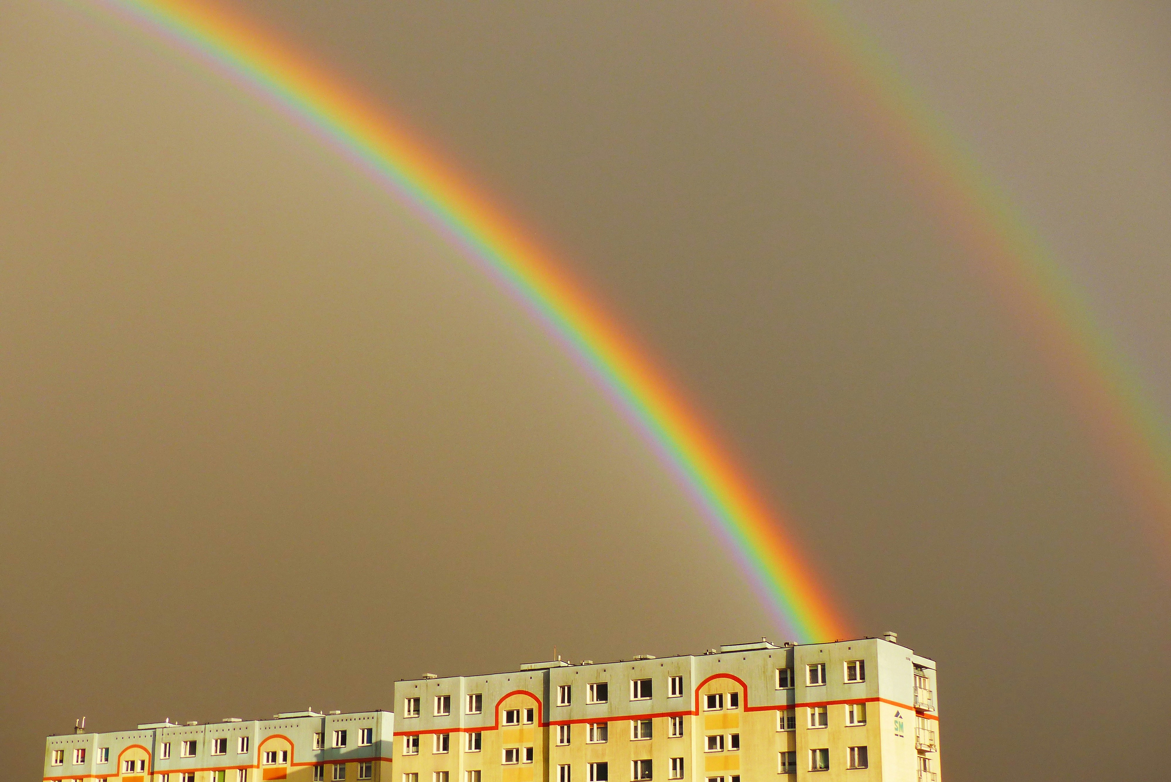 Vibrant rainbow arcs over a cityscape, contrasting with the moody sky and highlighting the architecture below.
