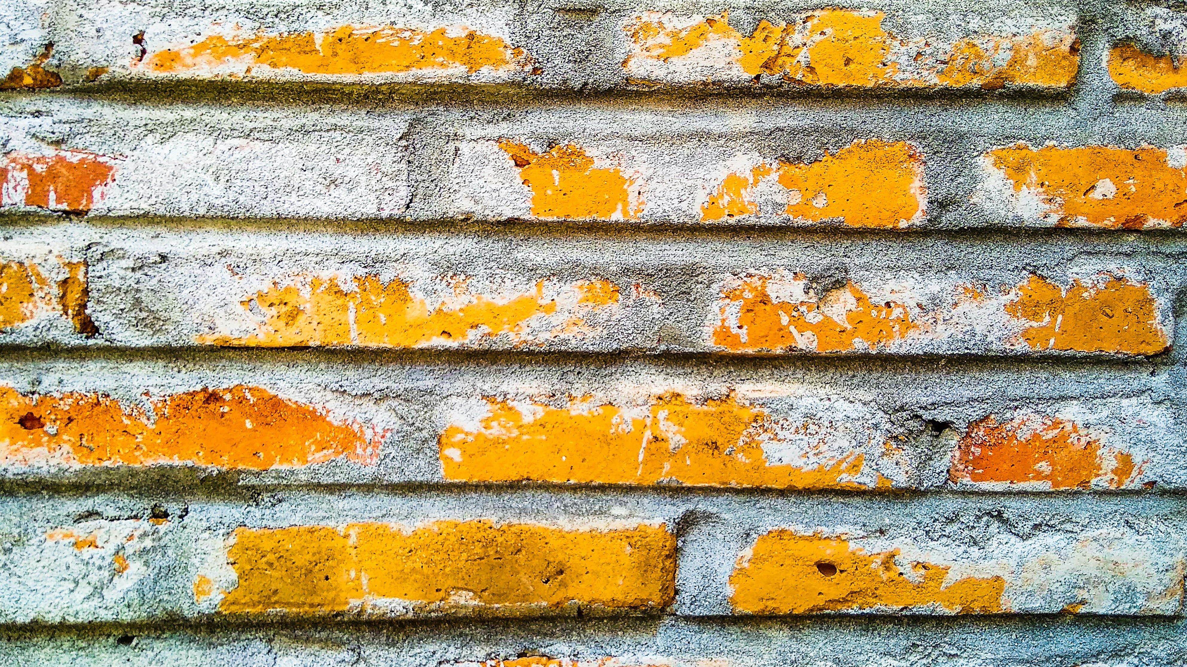 Weathered brick wall with irregular orange paint patches peeling across blue-gray mortar. The textured surface emphasizes urban grit and color variation.