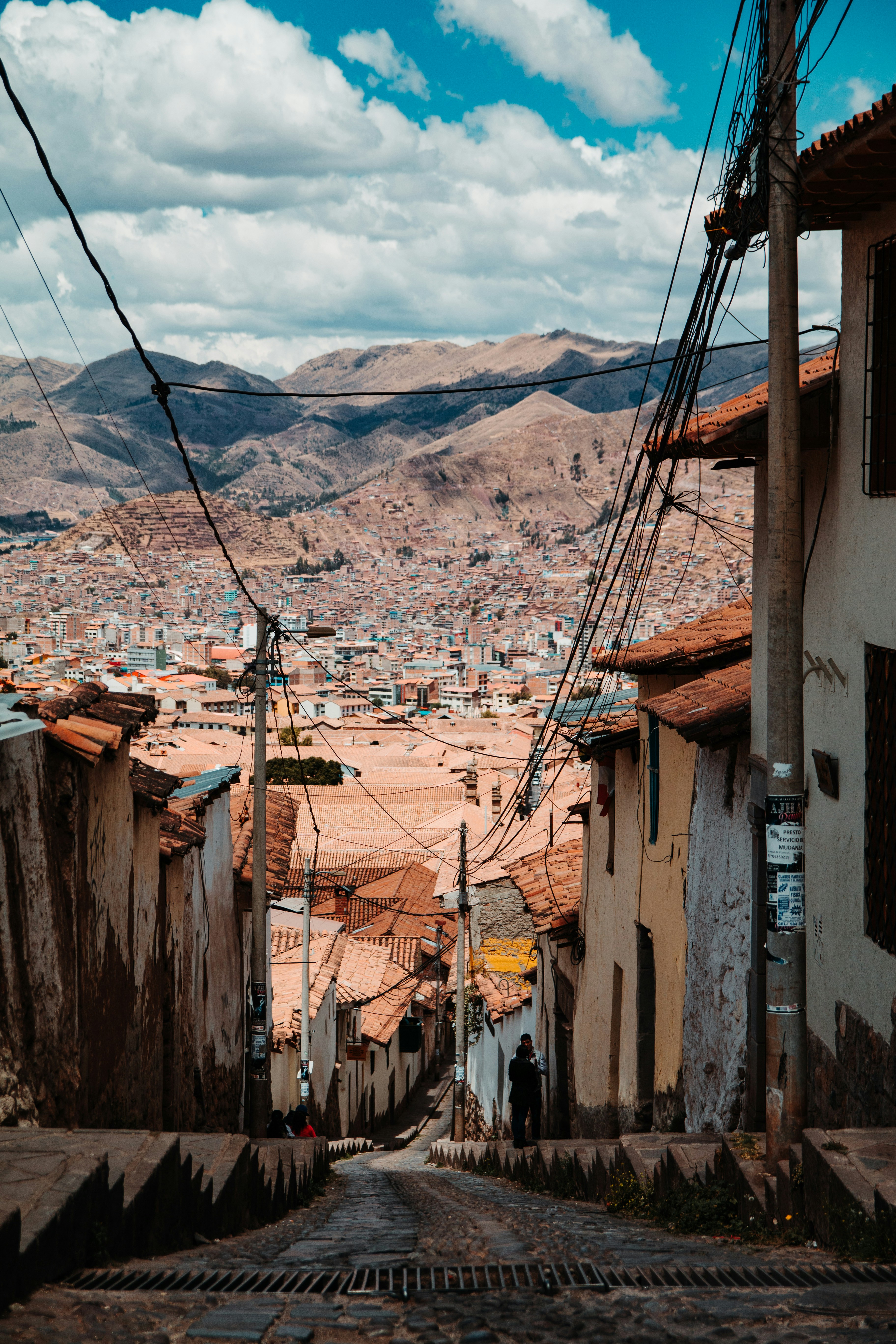A vibrant view of Cusco's terracotta rooftops and winding streets, framed by distant mountains under a dramatic sky.