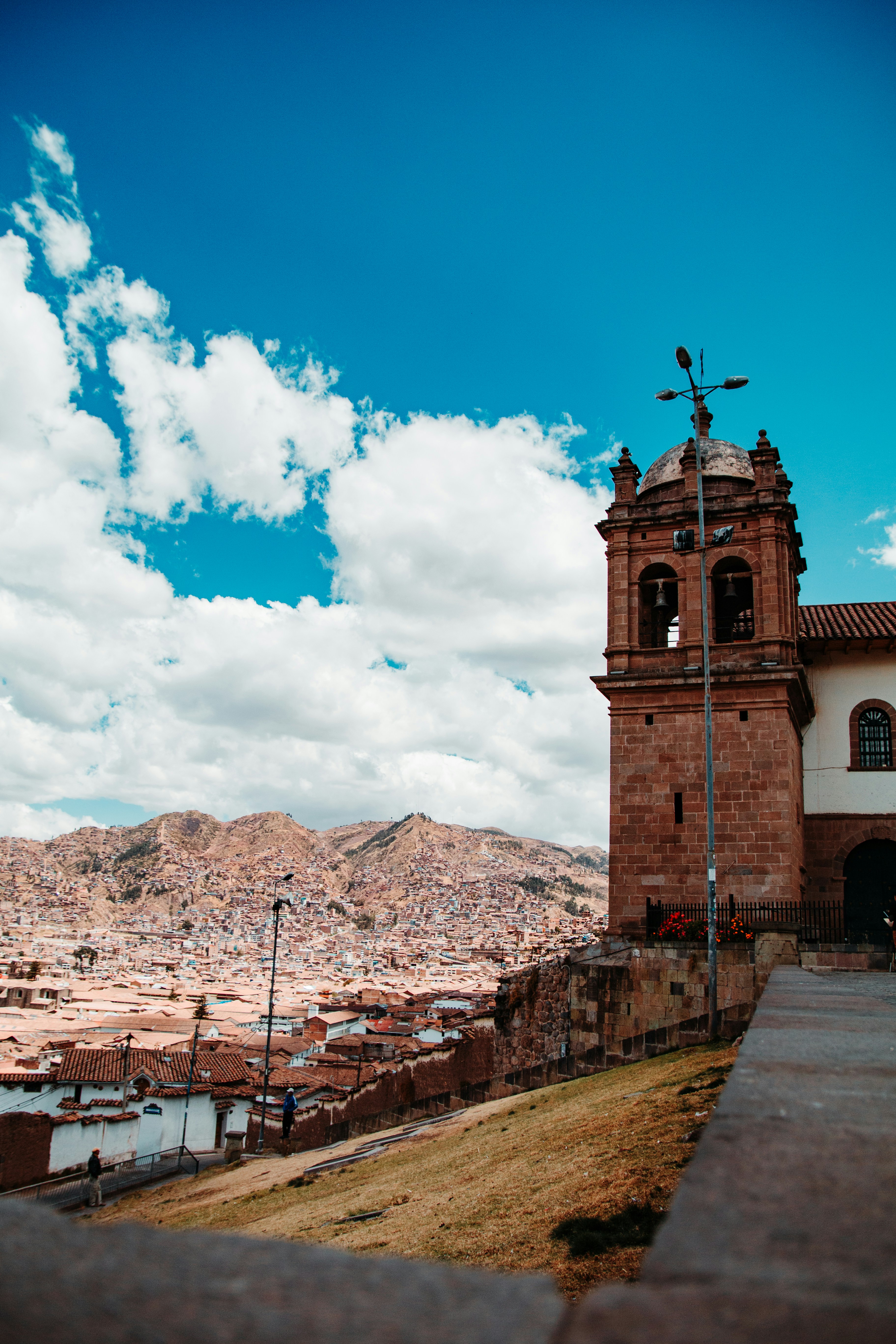 Historic church tower overlooking the sprawling city of Cusco against a backdrop of dramatic clouds and mountains.