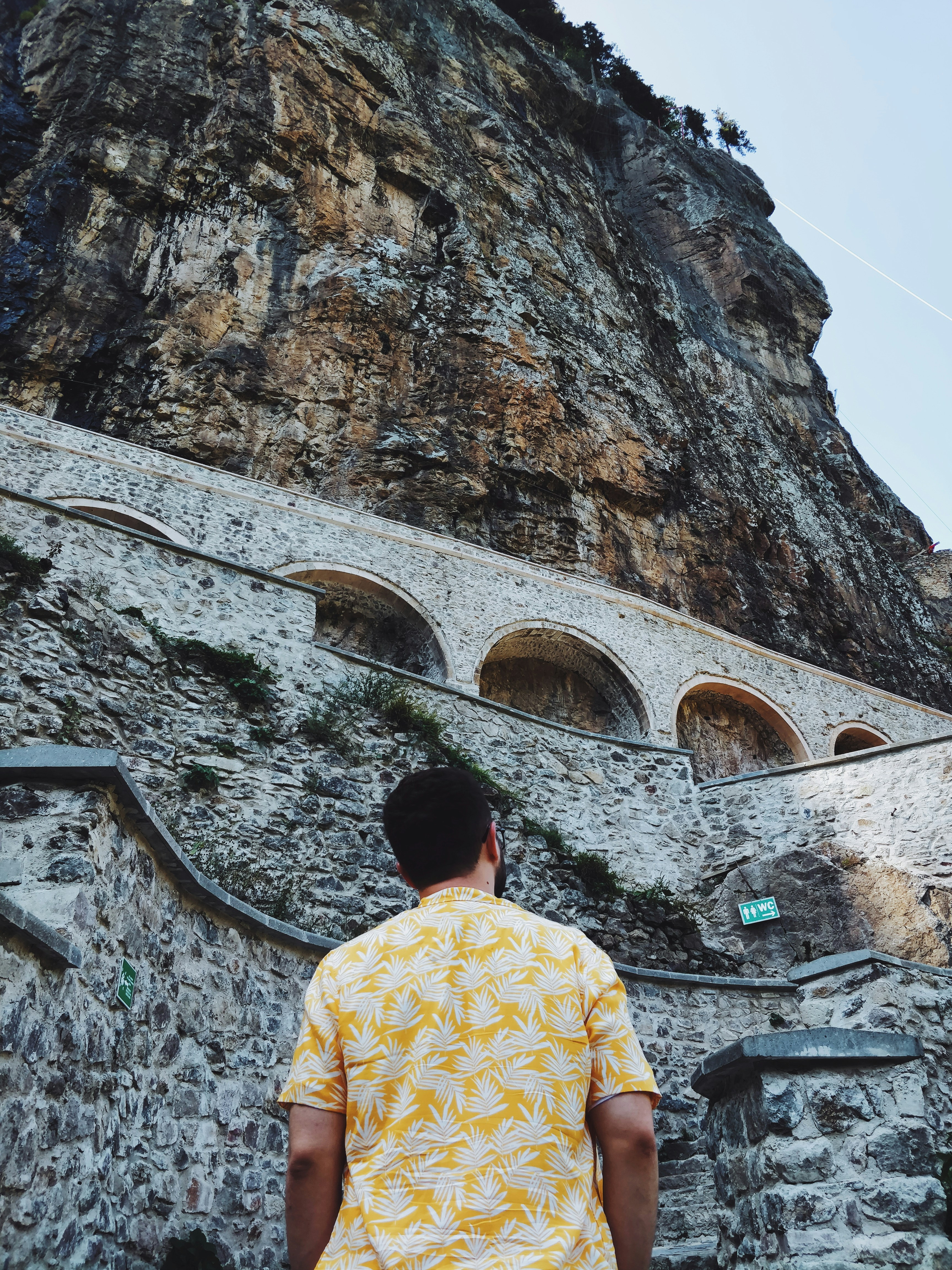 Back-Facing Traveler Beneath Cliffside Arched Viaducts