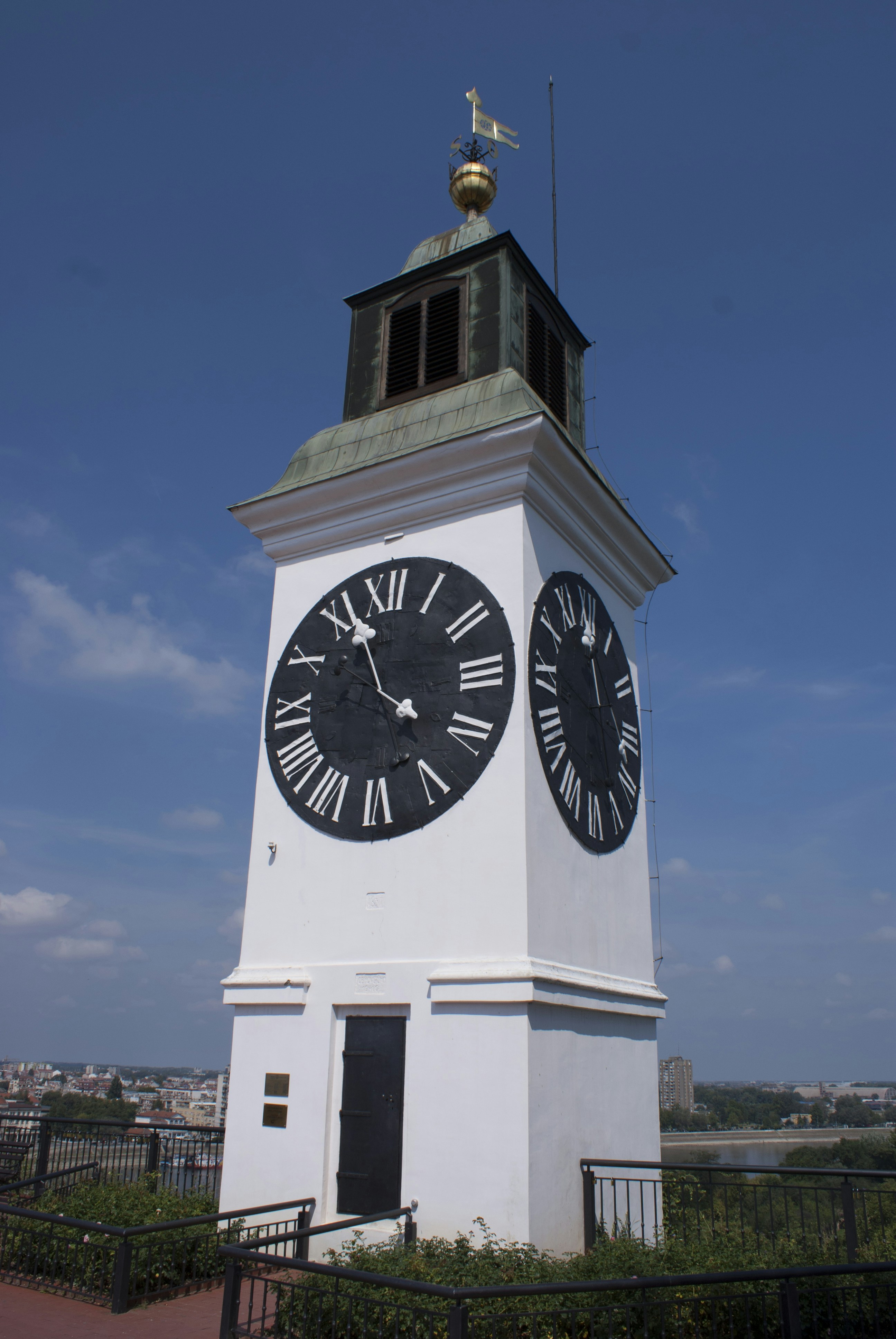 Historic clock tower with large black clock faces and Roman numerals against a clear blue sky. The structure stands as a landmark overlooking the city.