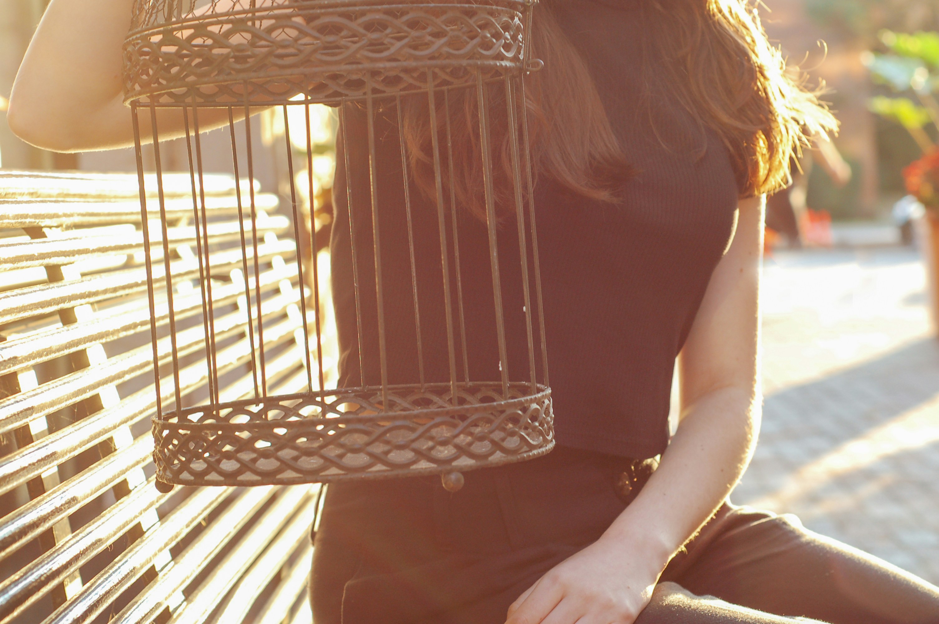 Sunlit Pause: A Woman with a Birdcage by the Park Bench