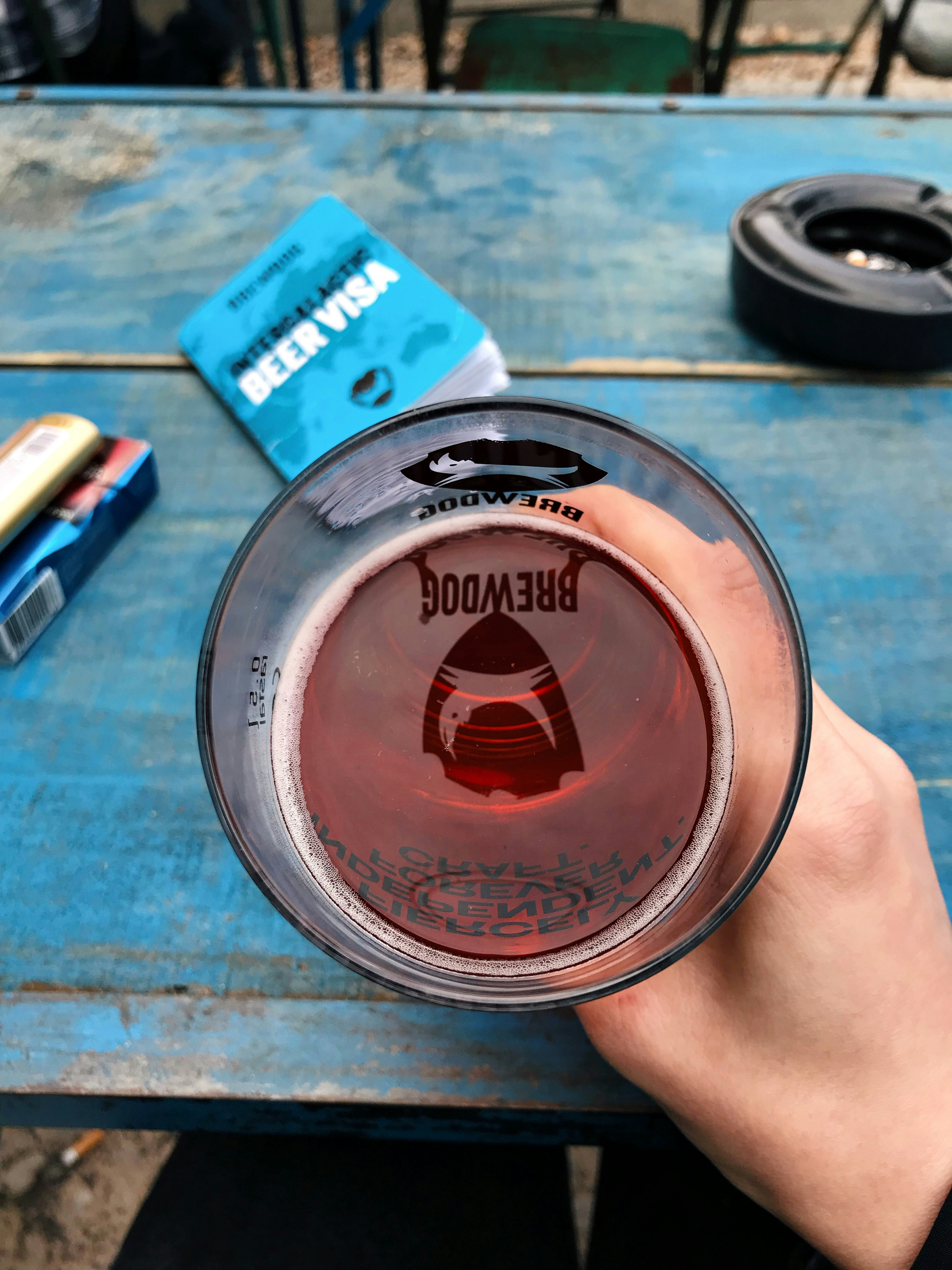 Crimson Reflection: A Pint Gripped Over a Weathered Blue Table