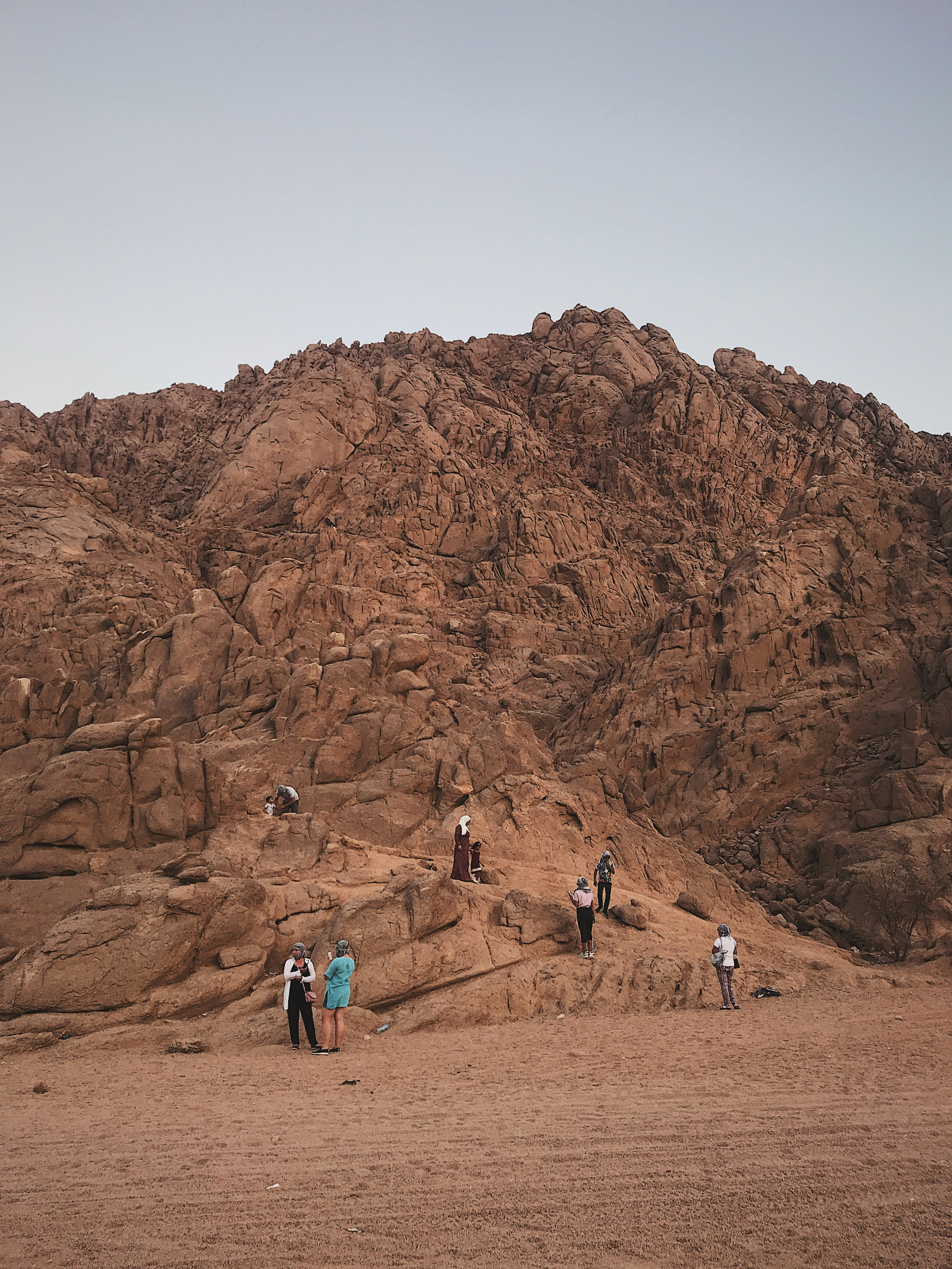Group of individuals exploring rocky terrain at dusk, showcasing the rugged beauty of the mountains. The scene captures a blend of human interaction with nature.