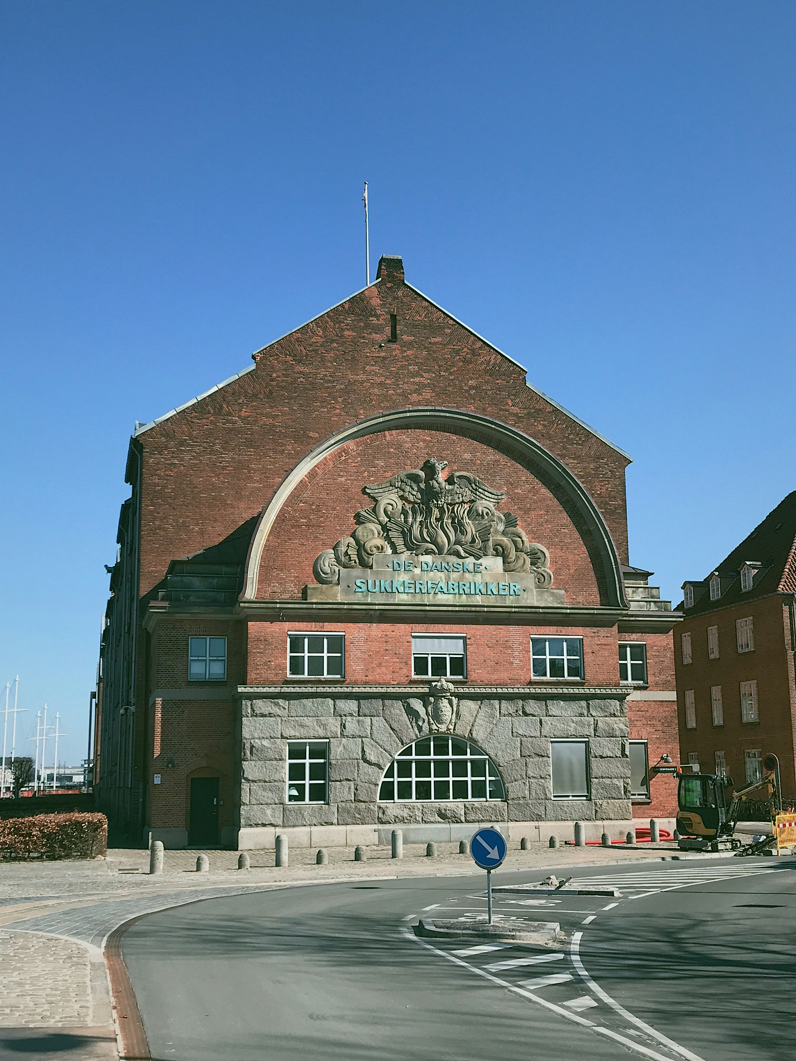 Historic brick building featuring intricate stonework and a prominent sign, set against a clear blue sky.