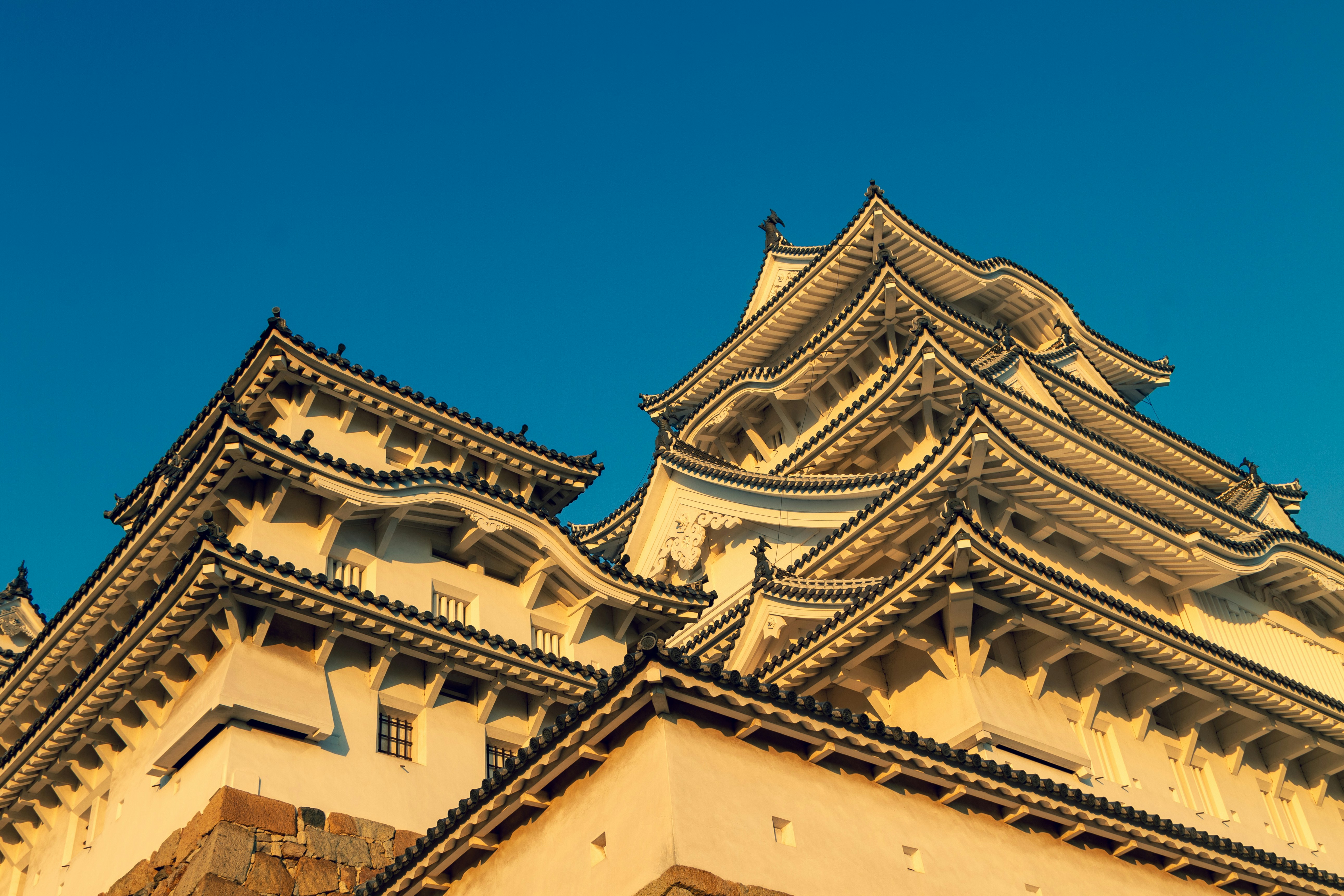 Traditional Japanese castle roof adorned with intricate details against a clear blue sky.