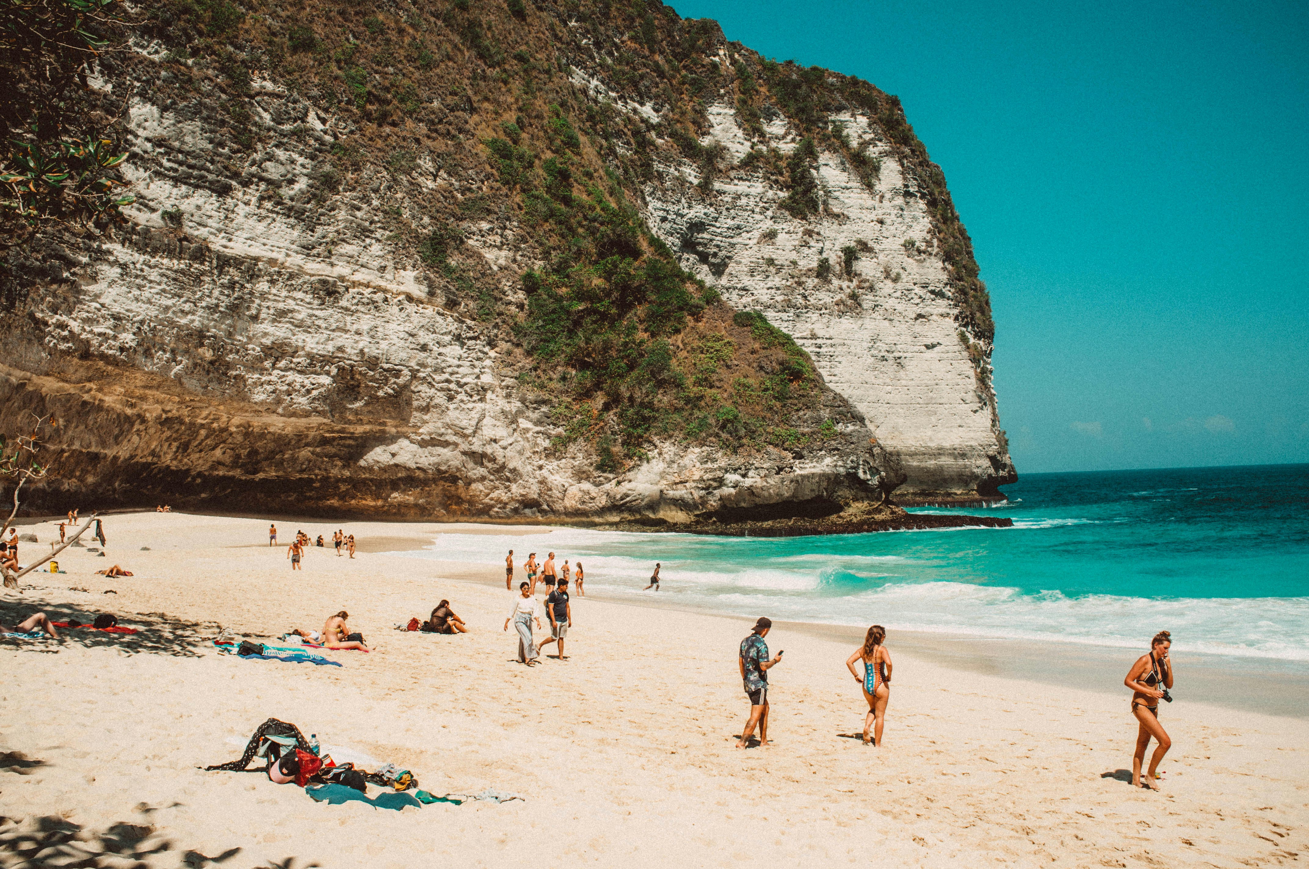 Visitors enjoying a sunny day on the sandy beach beneath towering cliffs and turquoise waters.