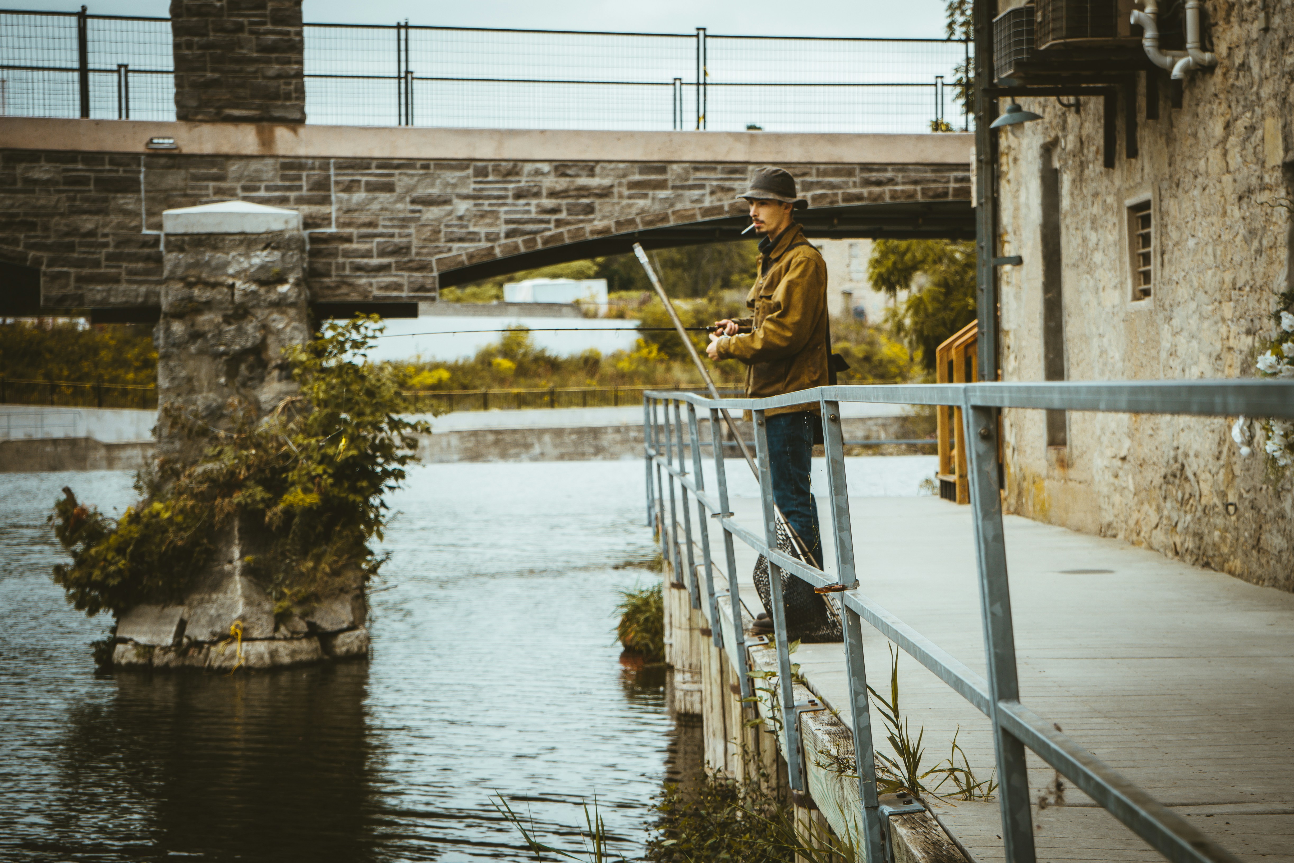 Angler on a Narrow Riverside Walk Under a Stone Bridge