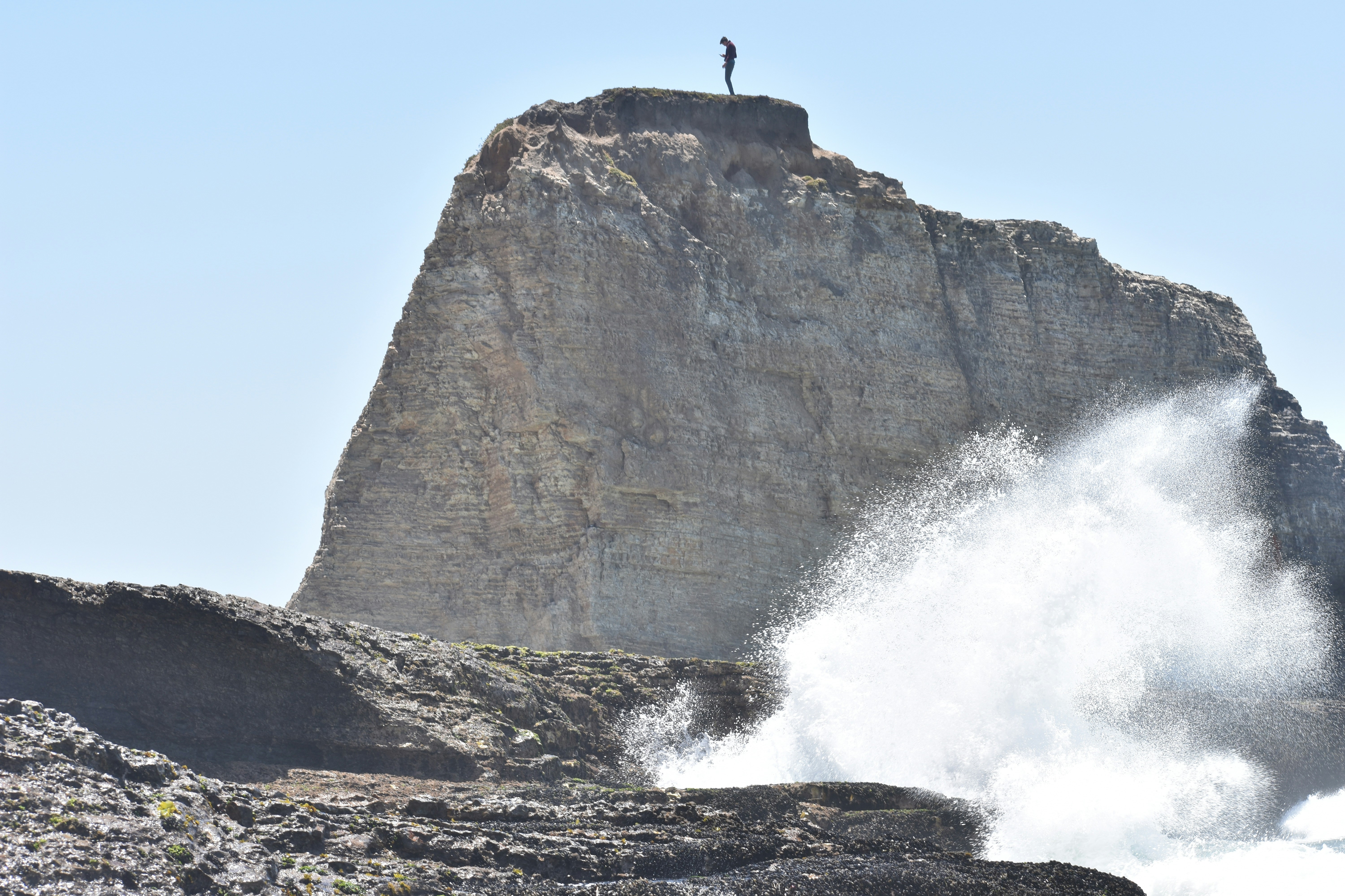 Clifftop Sentinel: A lone figure crowns a wind-swept promontory as waves collide