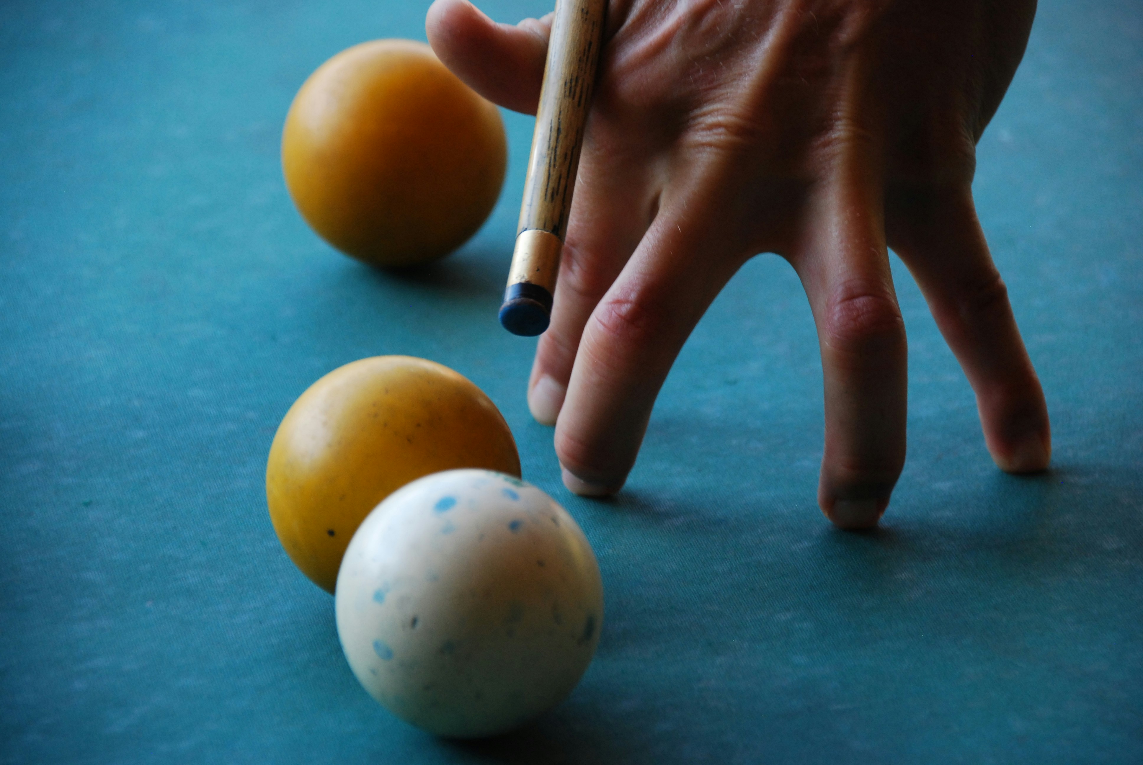 A hand poised with a cue stick reaches toward three billiard balls on a vibrant blue surface.