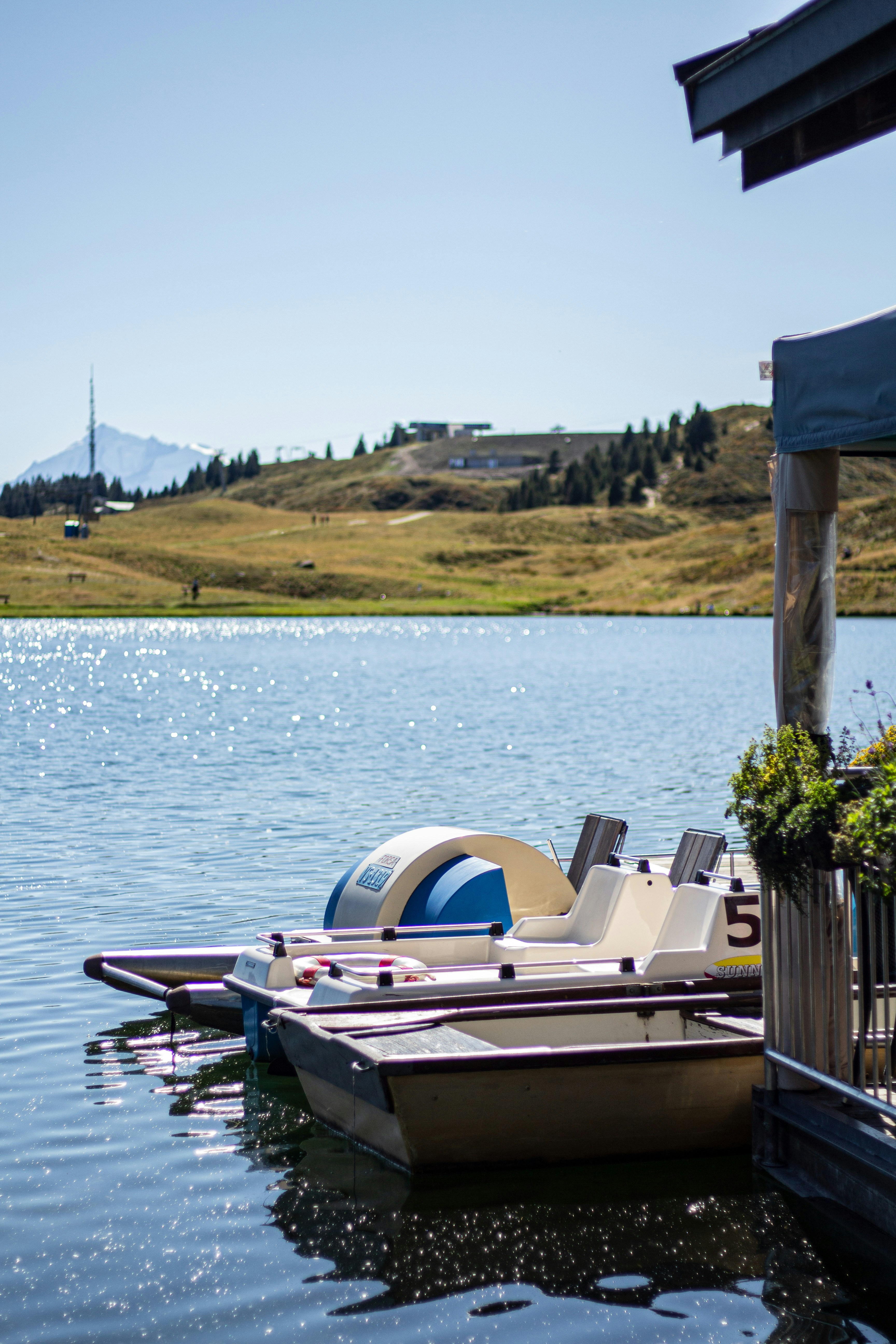 Pedal boats resting on a calm lake with lush hills in the background under a clear blue sky.