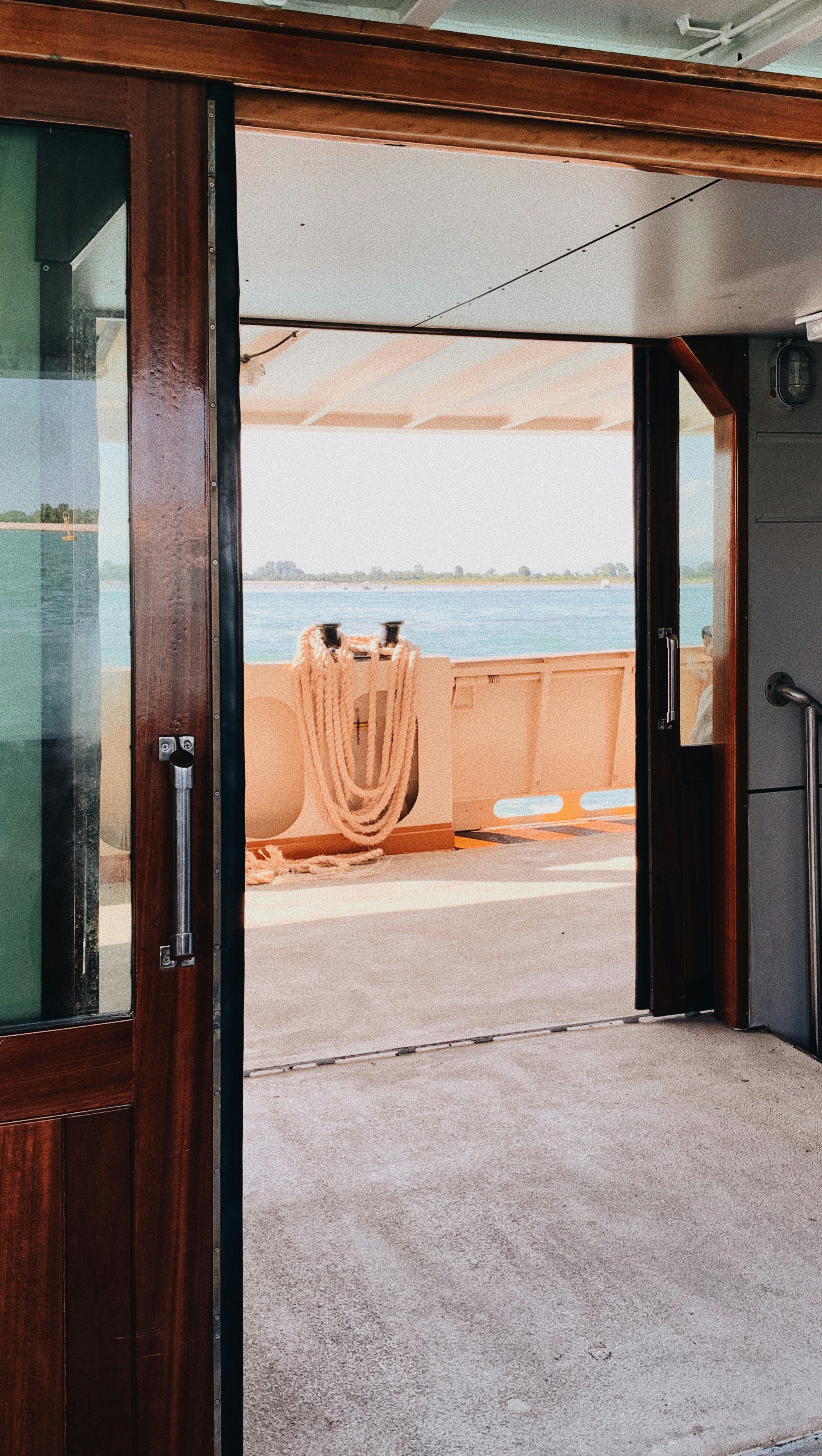 Interior doorway opens to a calm deck with a distant blue waterline and lounge chairs outside.