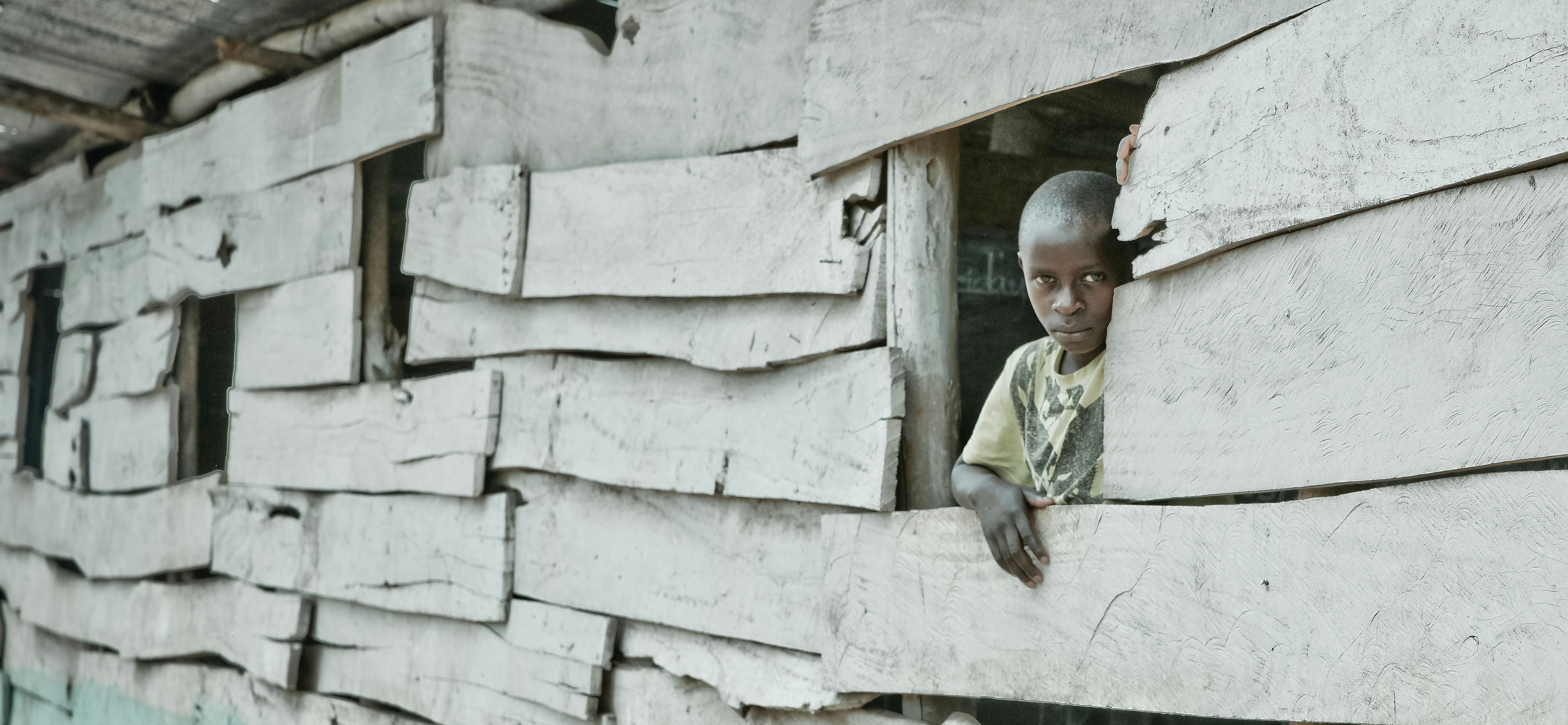 Child gazing out from a rustic wooden structure in a rural setting.