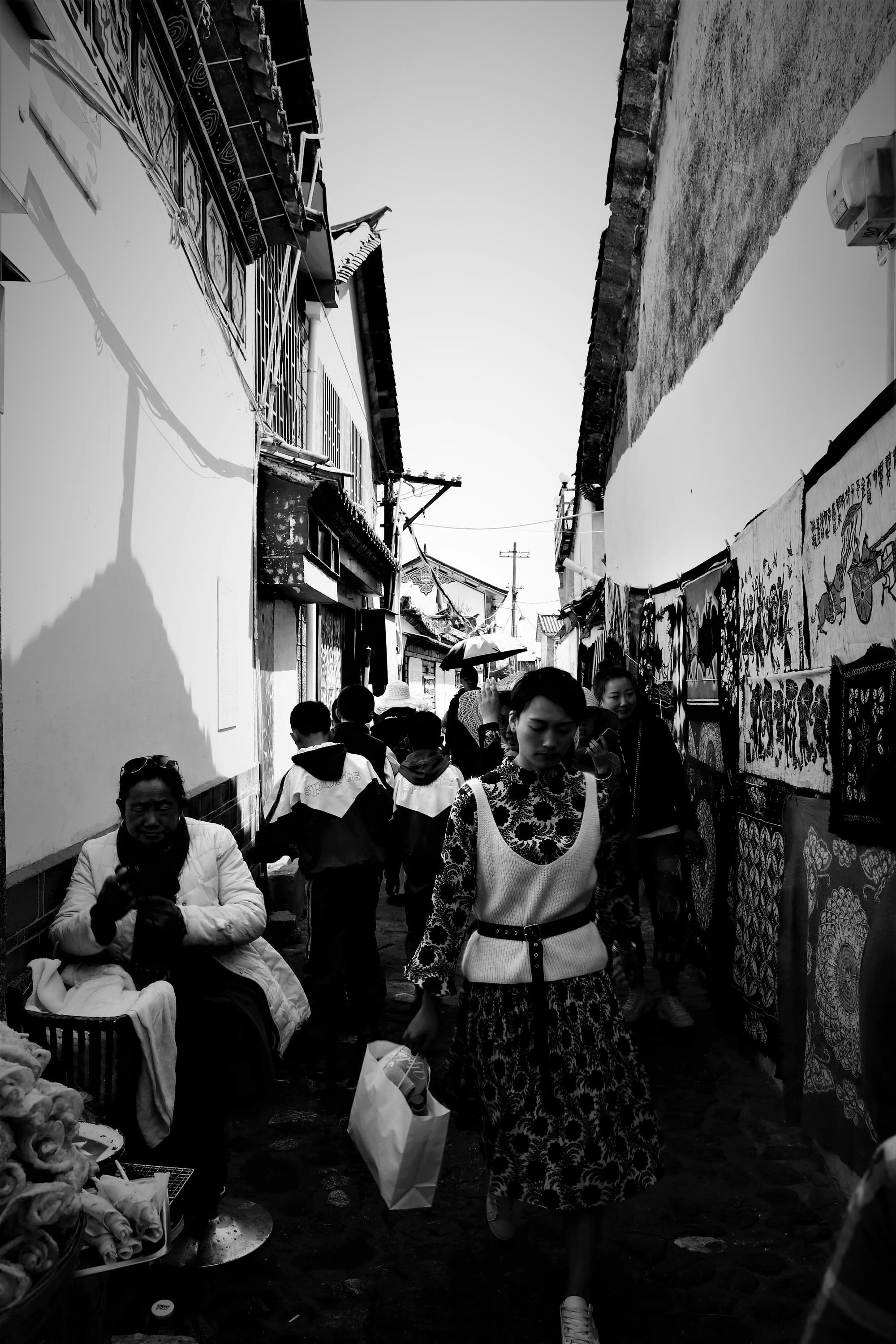 Monochrome Corridor: A Patterned Dress Leads Through a Crowded Alley