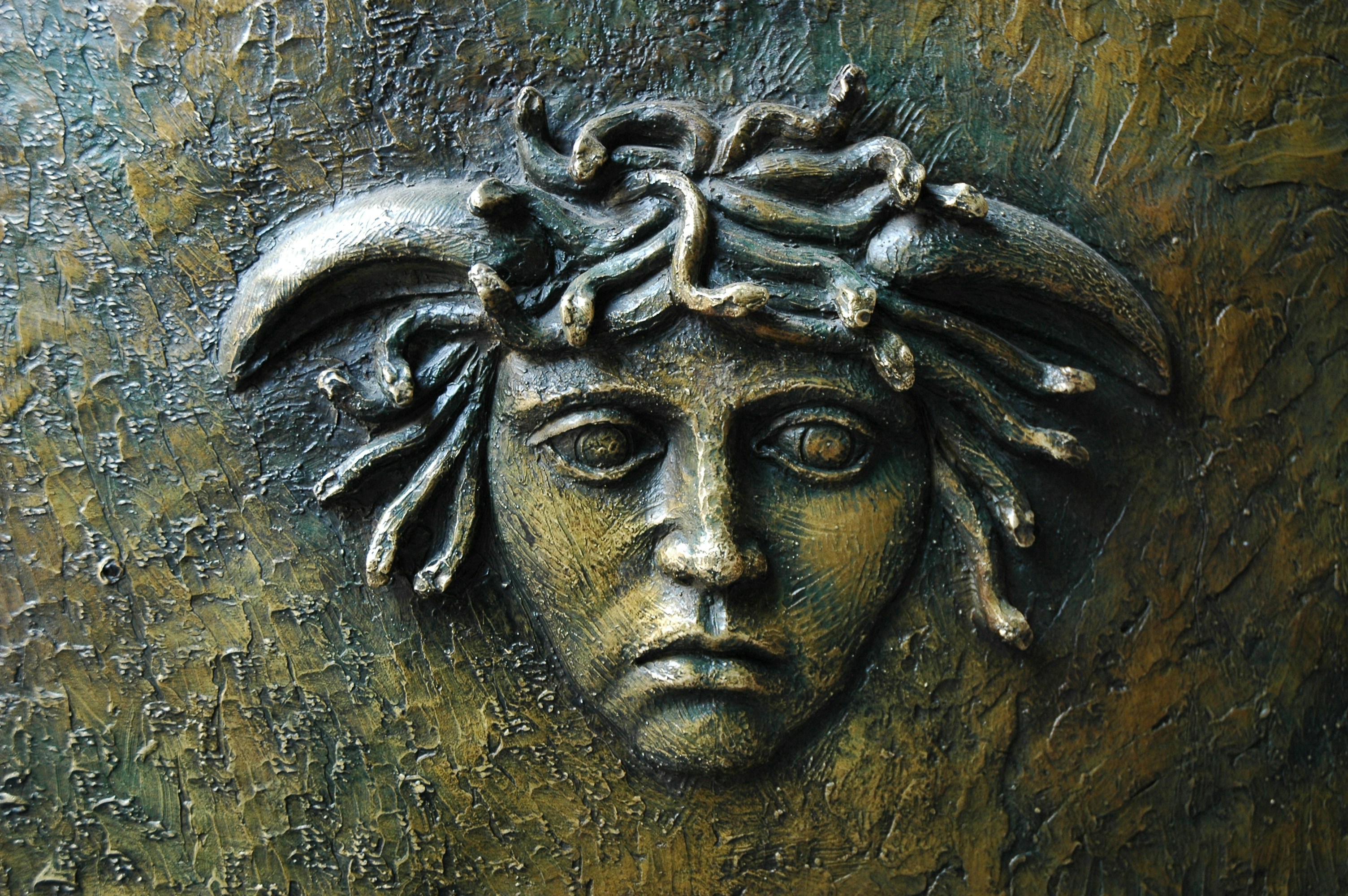 Intricate bronze relief depicting a gorgon's face with serpentine hair, capturing a moment of stillness and intensity.