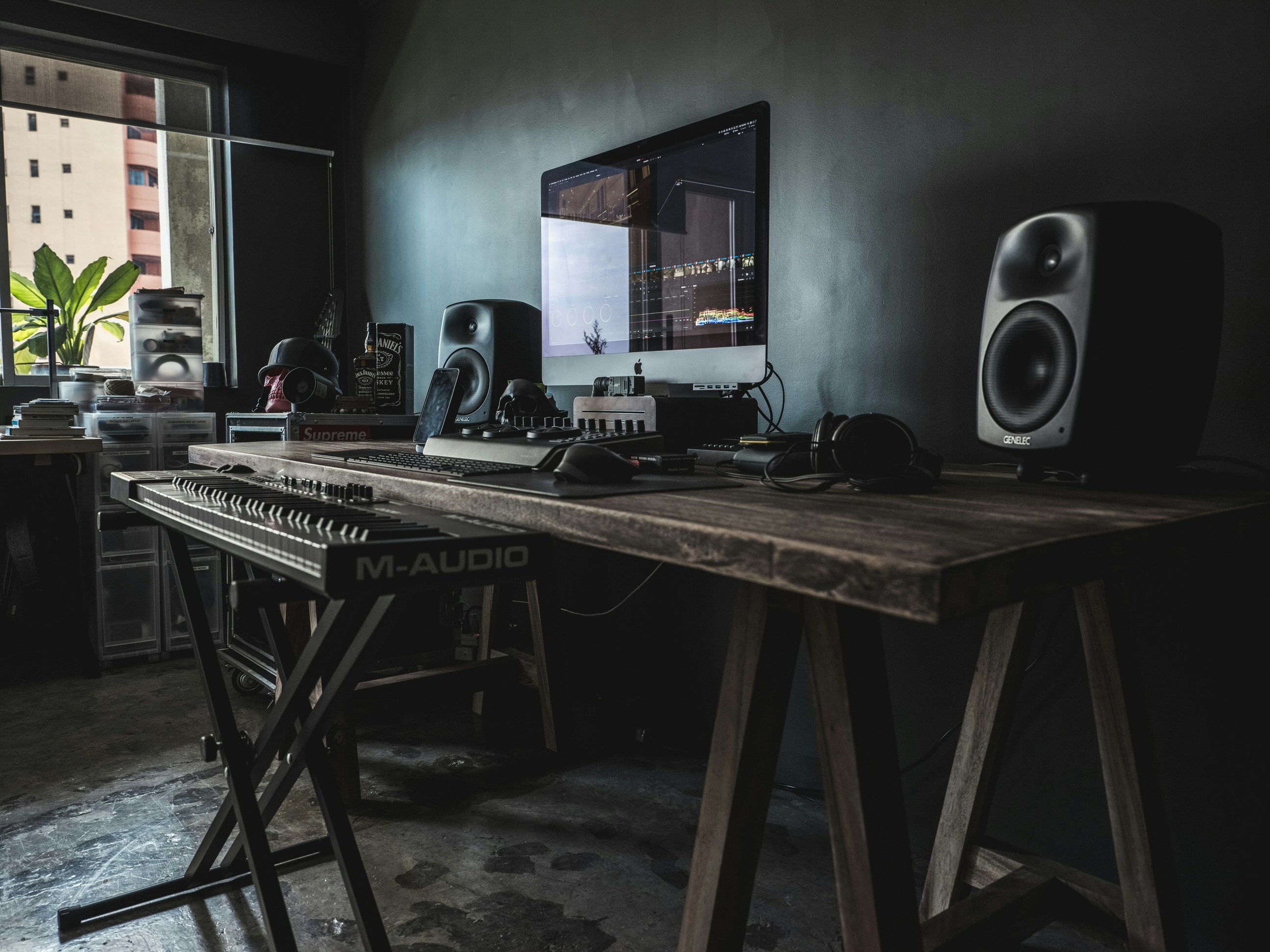 Wooden desk with music production equipment, speakers, and a computer in a dimly lit room.