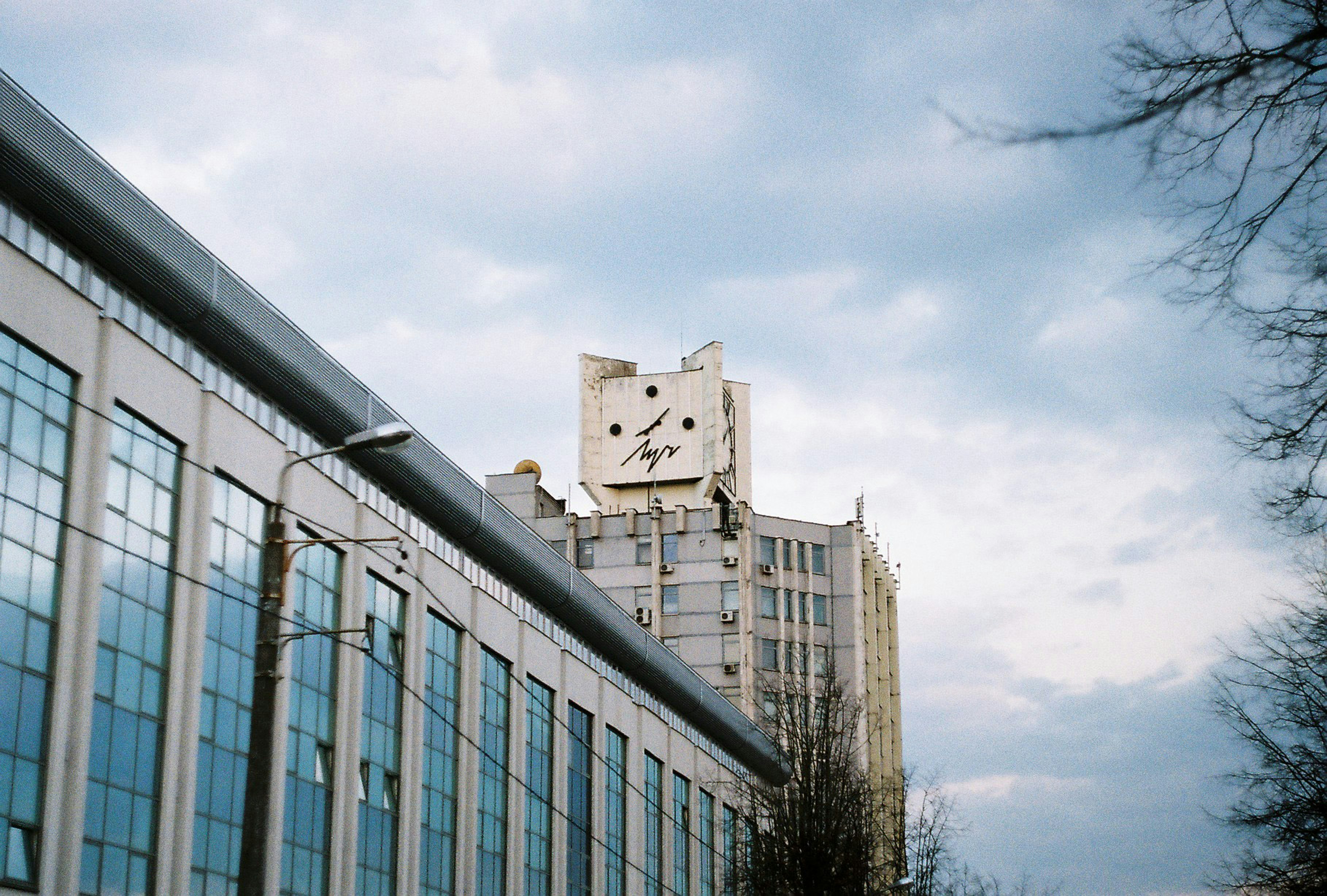 A tall building featuring a clock tower looms over a contemporary glass structure, showcasing urban evolution. The cloudy sky adds a dramatic backdrop.