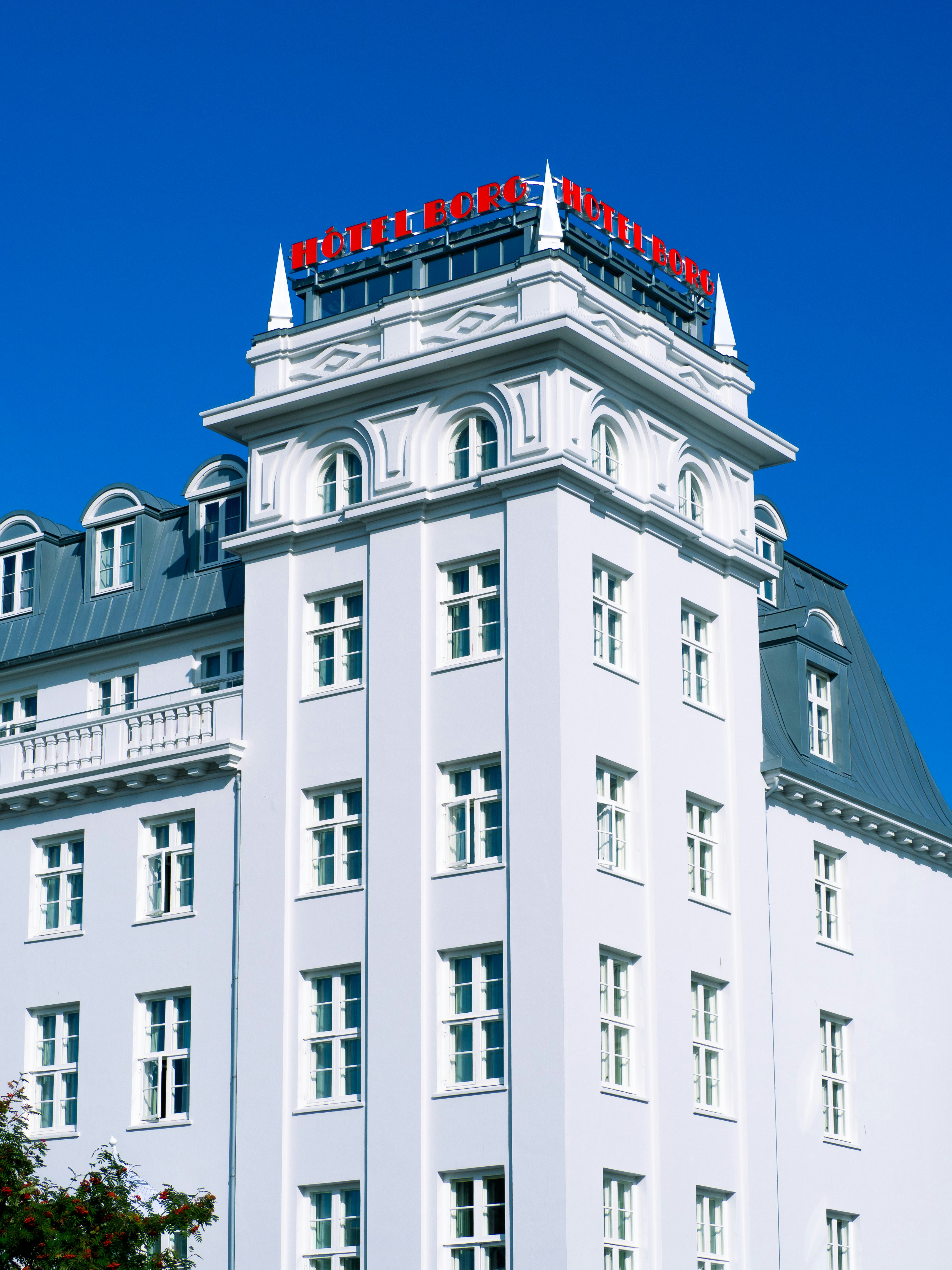 Stately white-hued hotel tower crowned with red signage against a cobalt sky