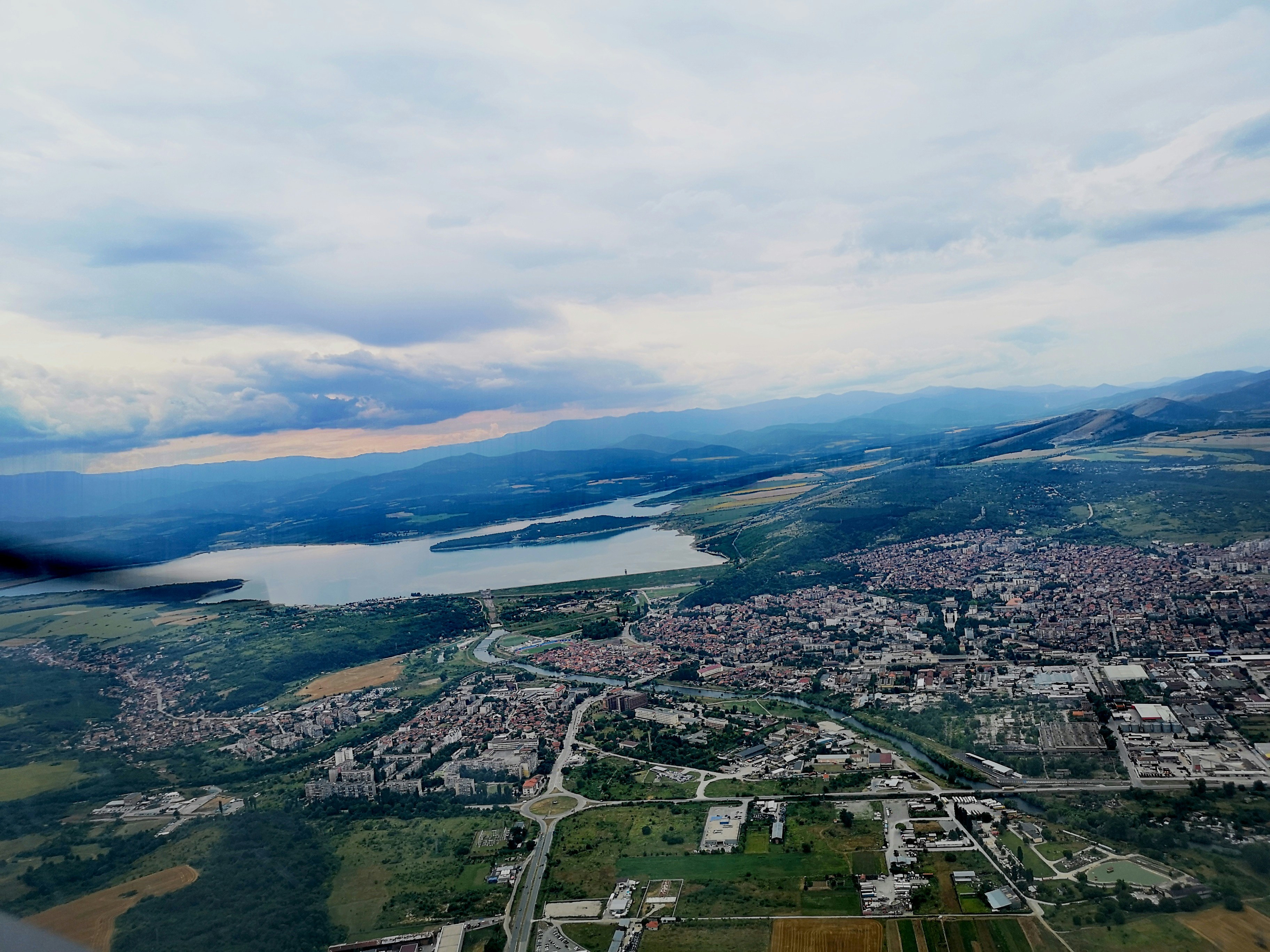 Expansive view of a cityscape merging with lush greenery and a serene lake, captured from above. The image showcases the interplay between urban development and natural beauty.