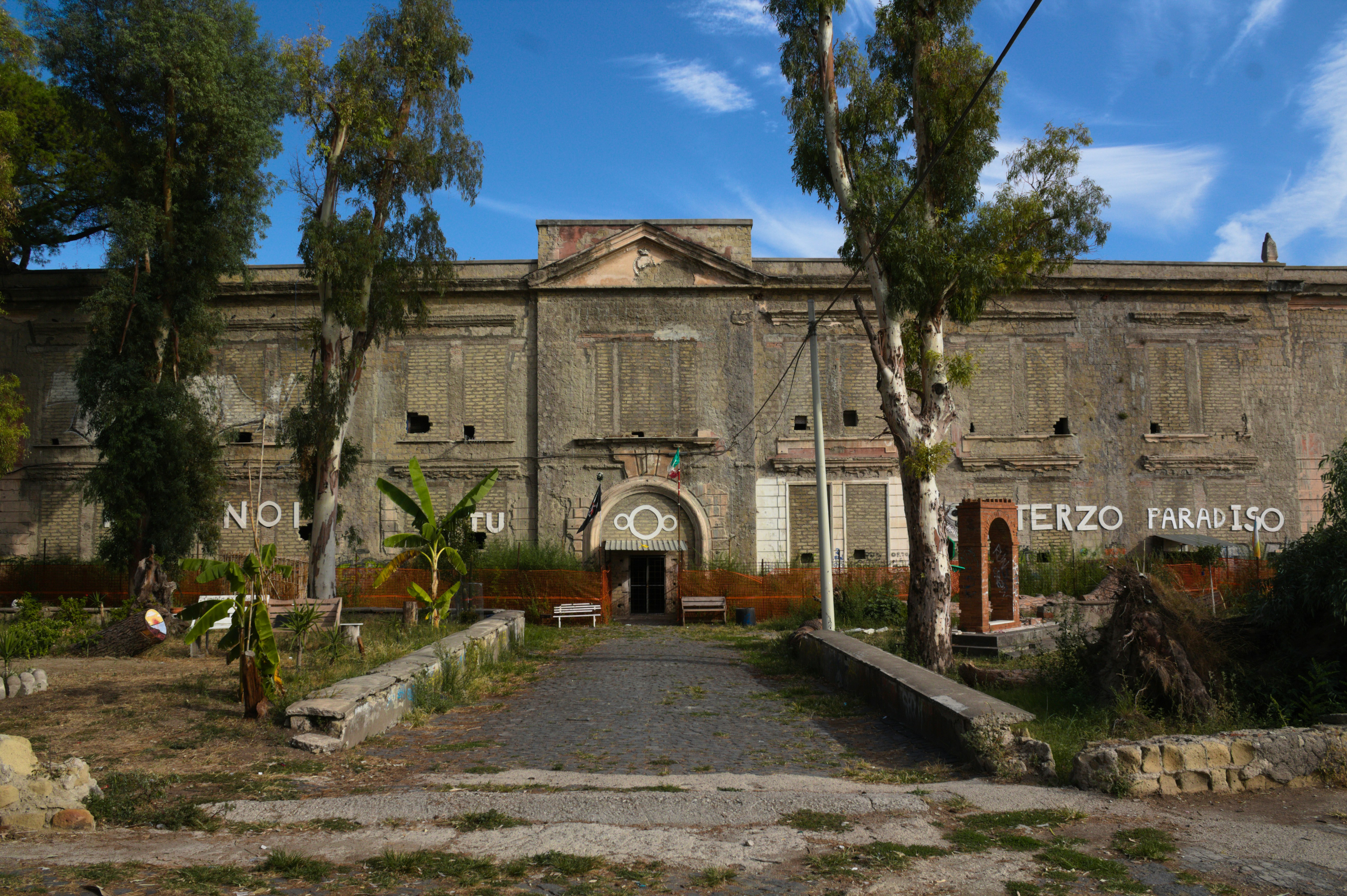 Old stone building facade with trees and plants under a blue sky.