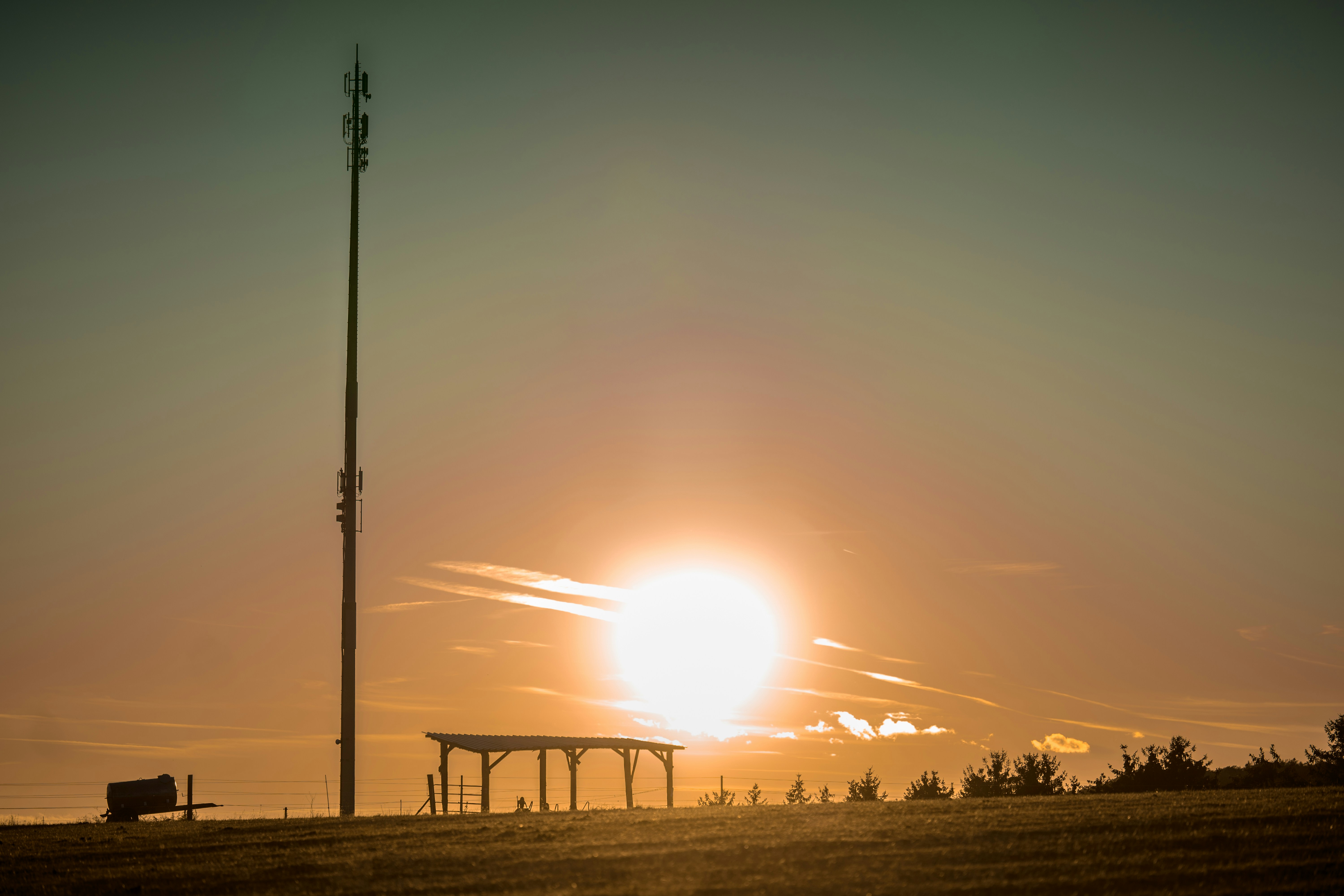 Silhouetted structures and a lone pole under a vibrant sunrise sky.