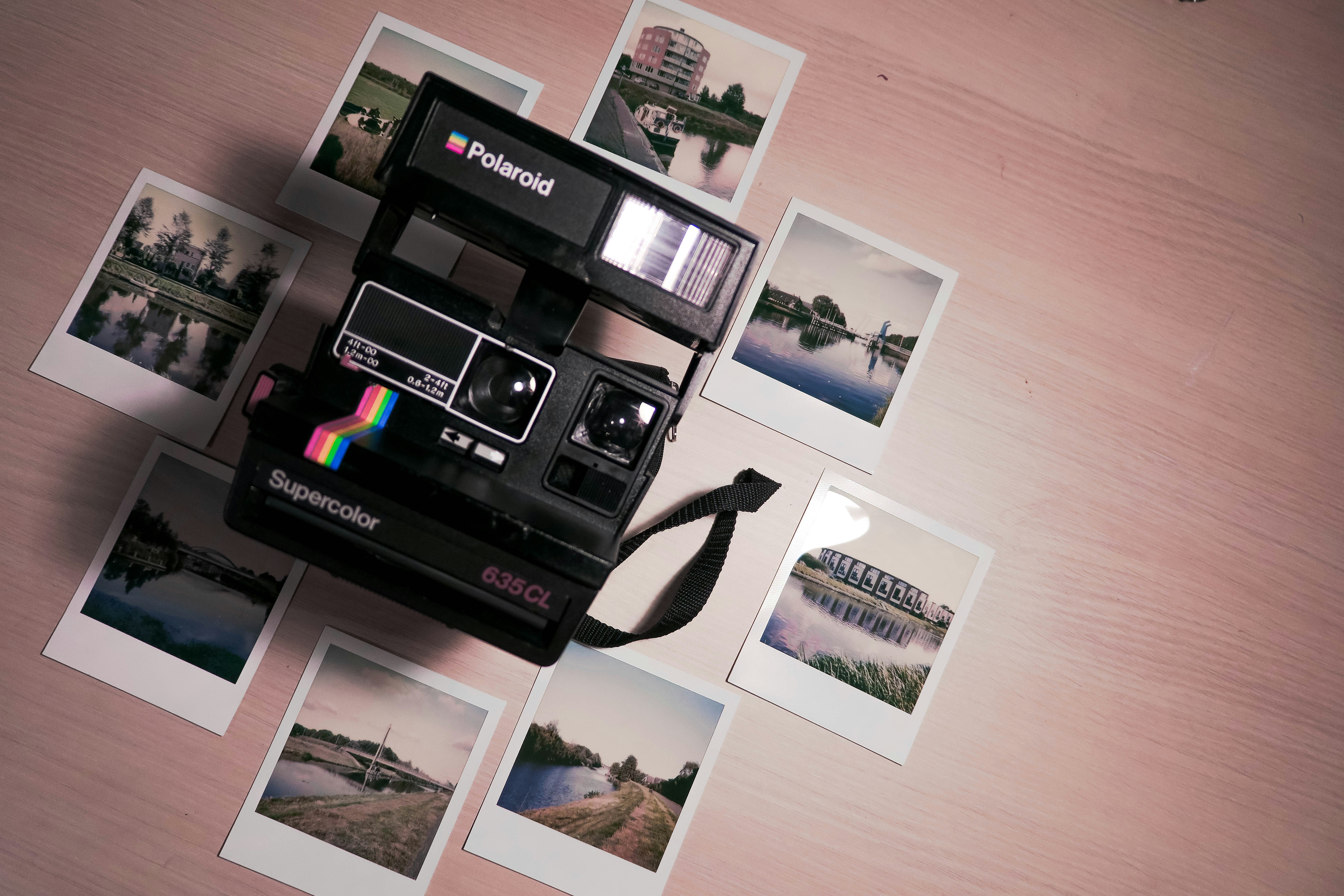A vintage Polaroid instant camera rests on a wooden surface, surrounded by scattered prints.
