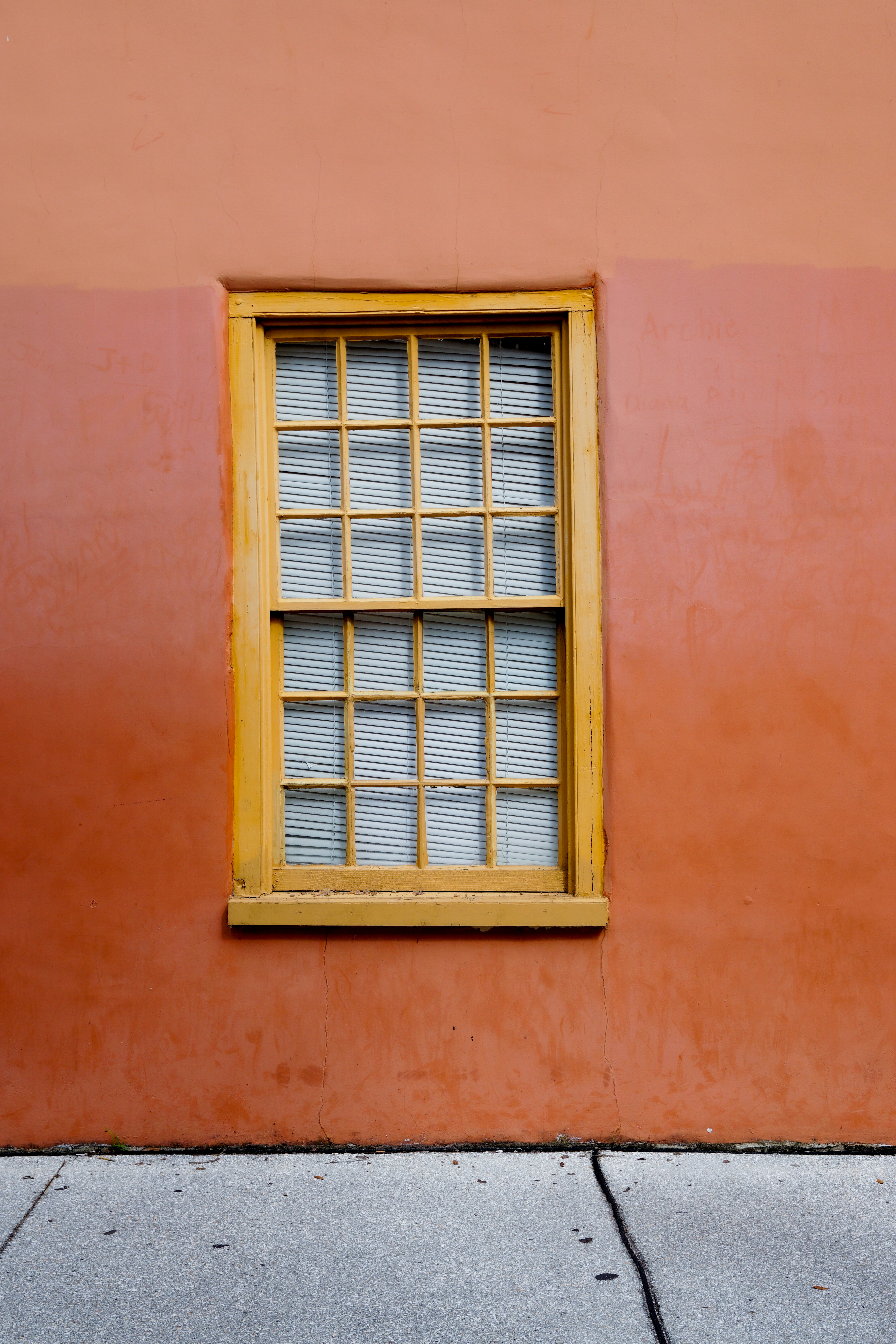 A vintage window framed in bright yellow, set against a textured orange wall, showcasing architectural charm and color contrast.