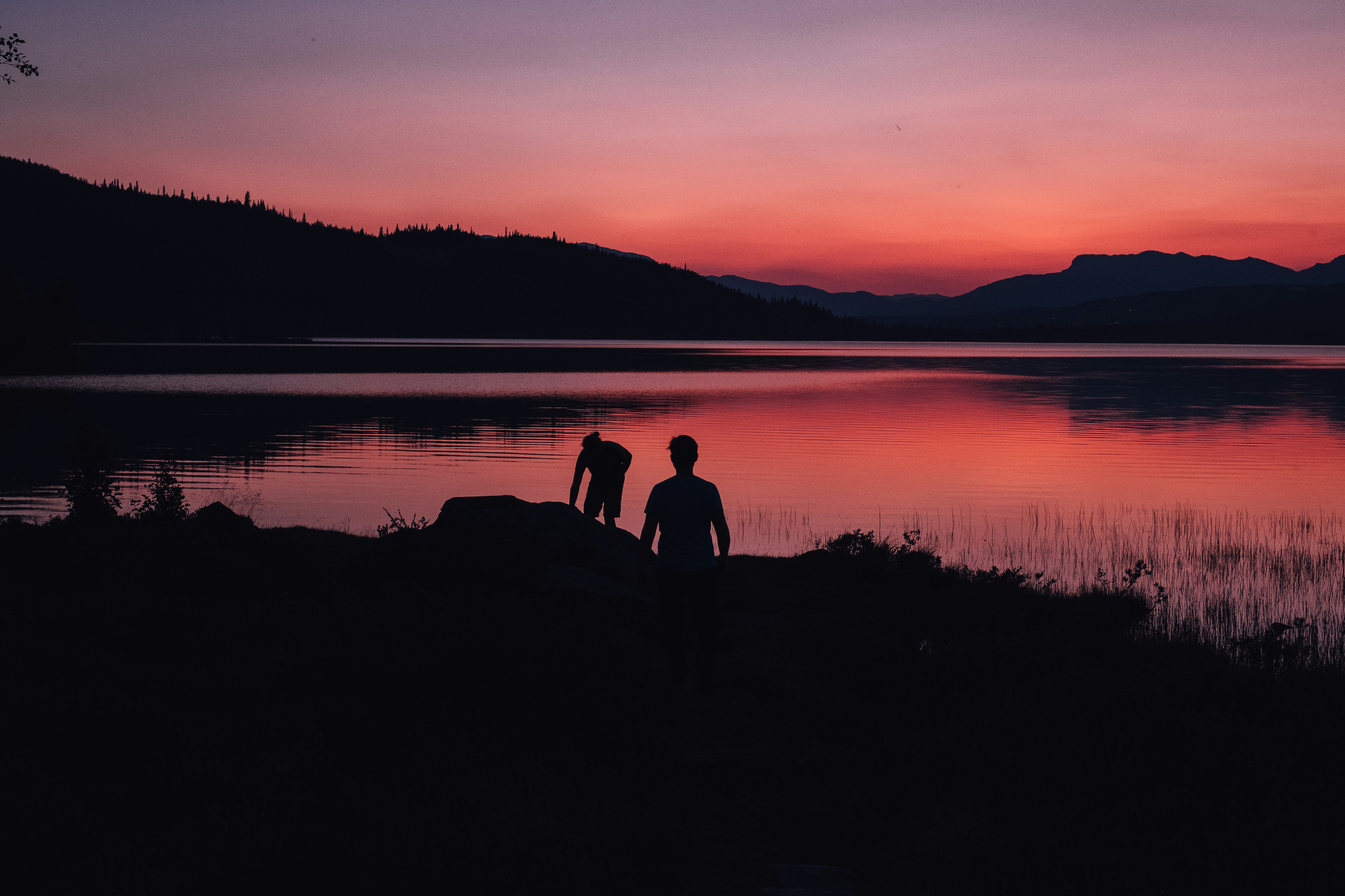 Silhouetted figures near a tranquil lake at twilight, with vibrant hues reflecting on the water's surface.