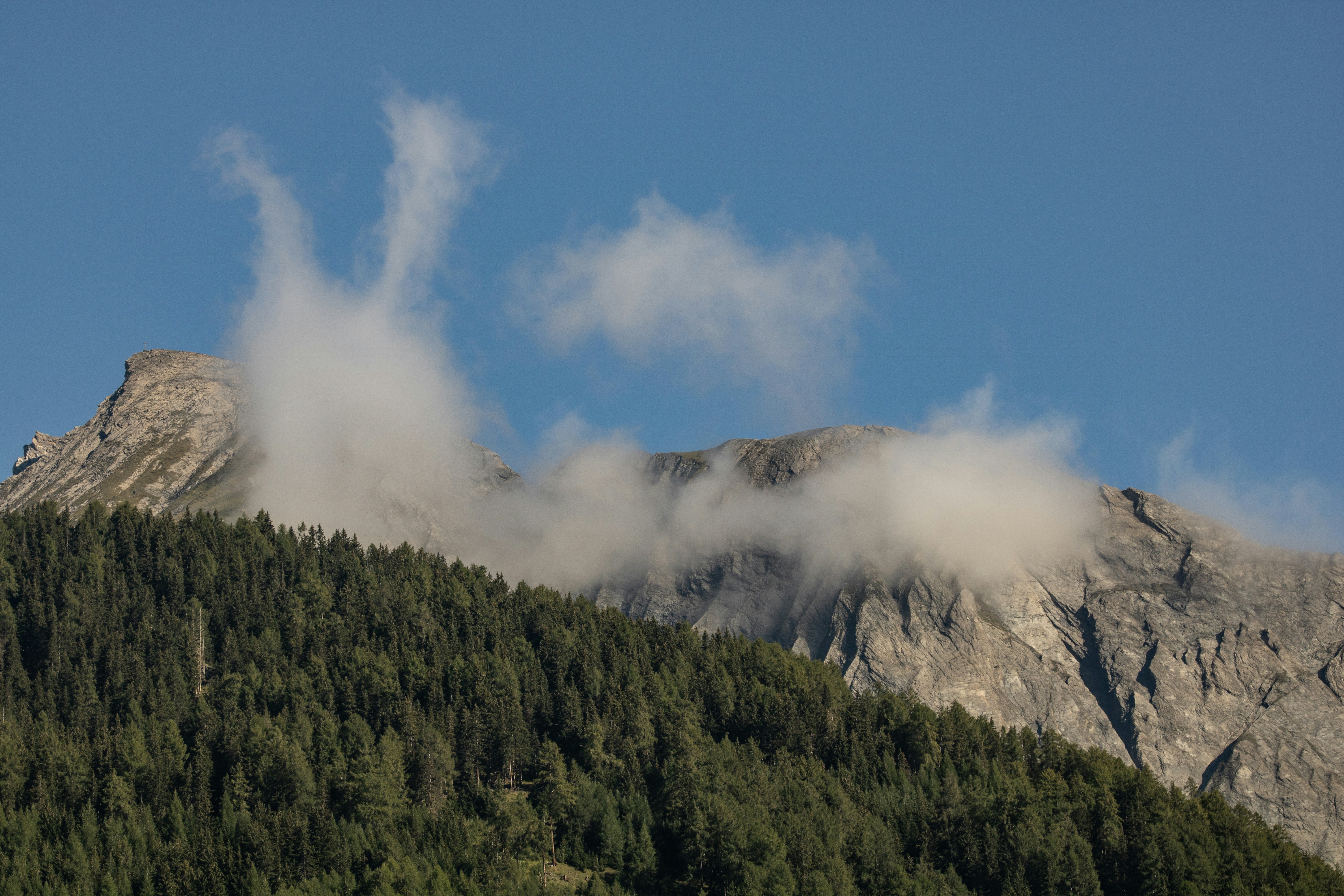 Fluffy clouds drift over a rugged mountain landscape, highlighting the contrast between the lush greenery and rocky peaks.