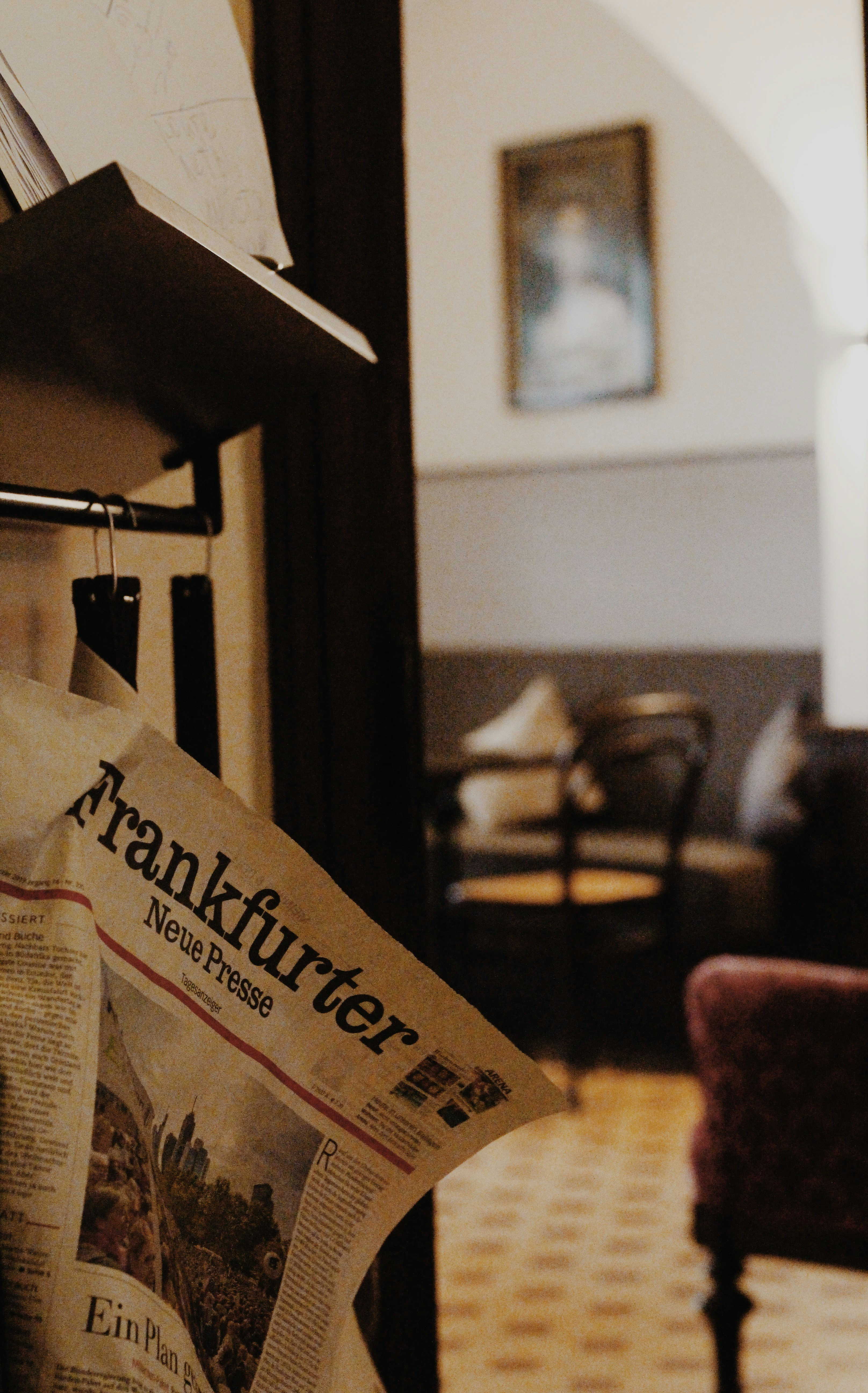 A vintage newspaper hangs on a wall, leading the eye into a cozy café setting with soft seating and warm tones.