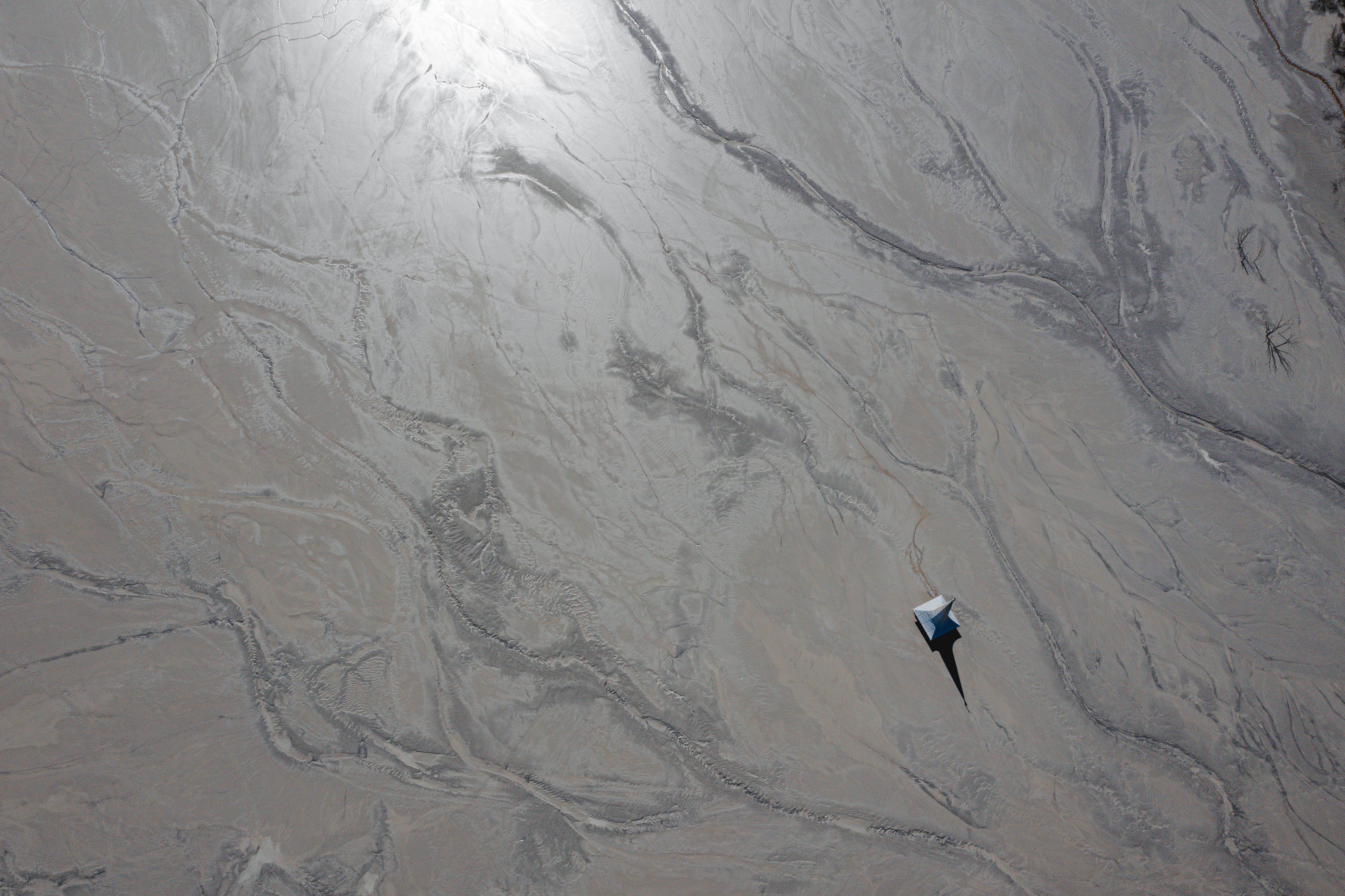 A lone sailboat glides across a vast expanse of shimmering, textured water, reflecting the sunlight in a serene landscape.