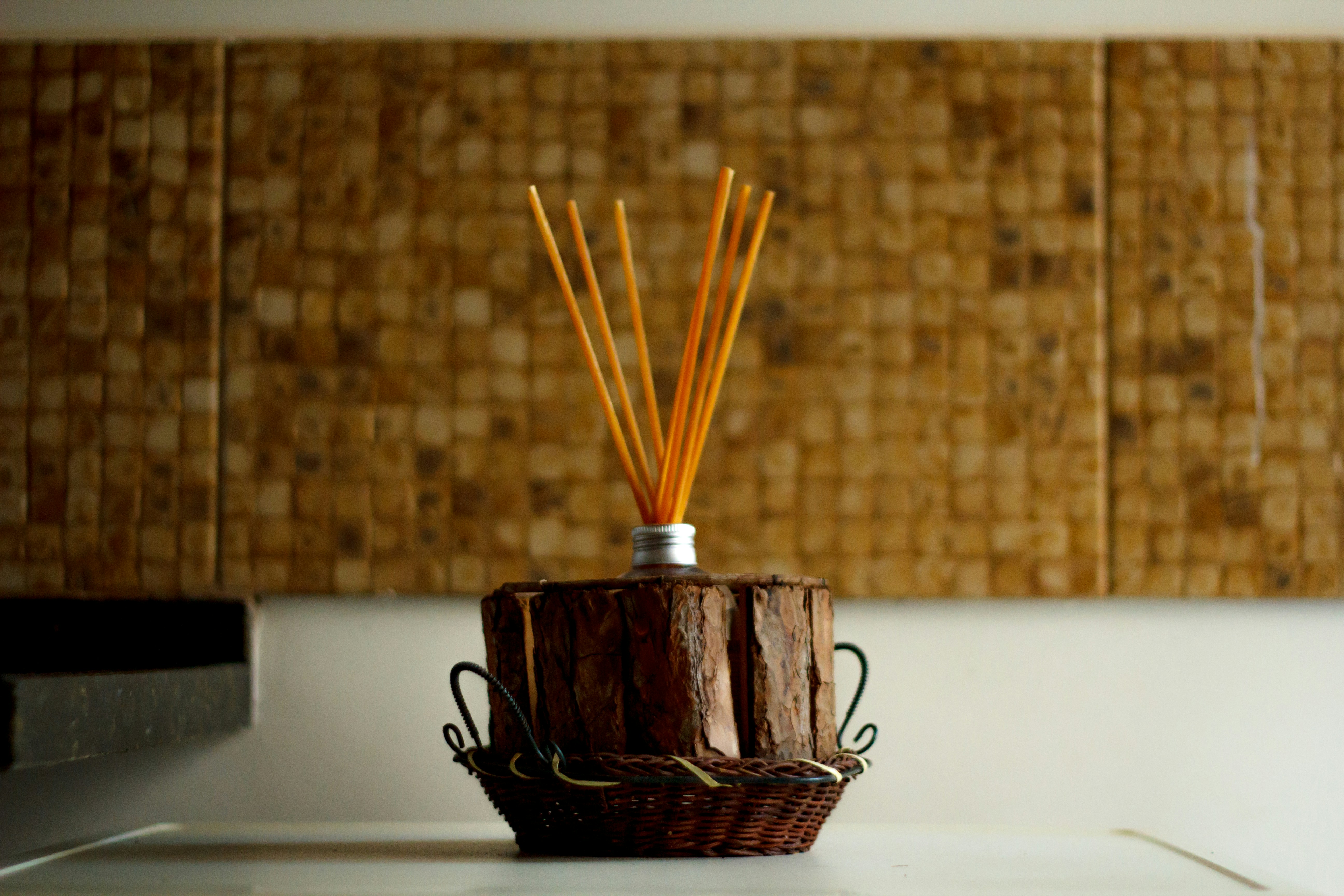 Reed diffuser in a wooden holder against a tiled backsplash.