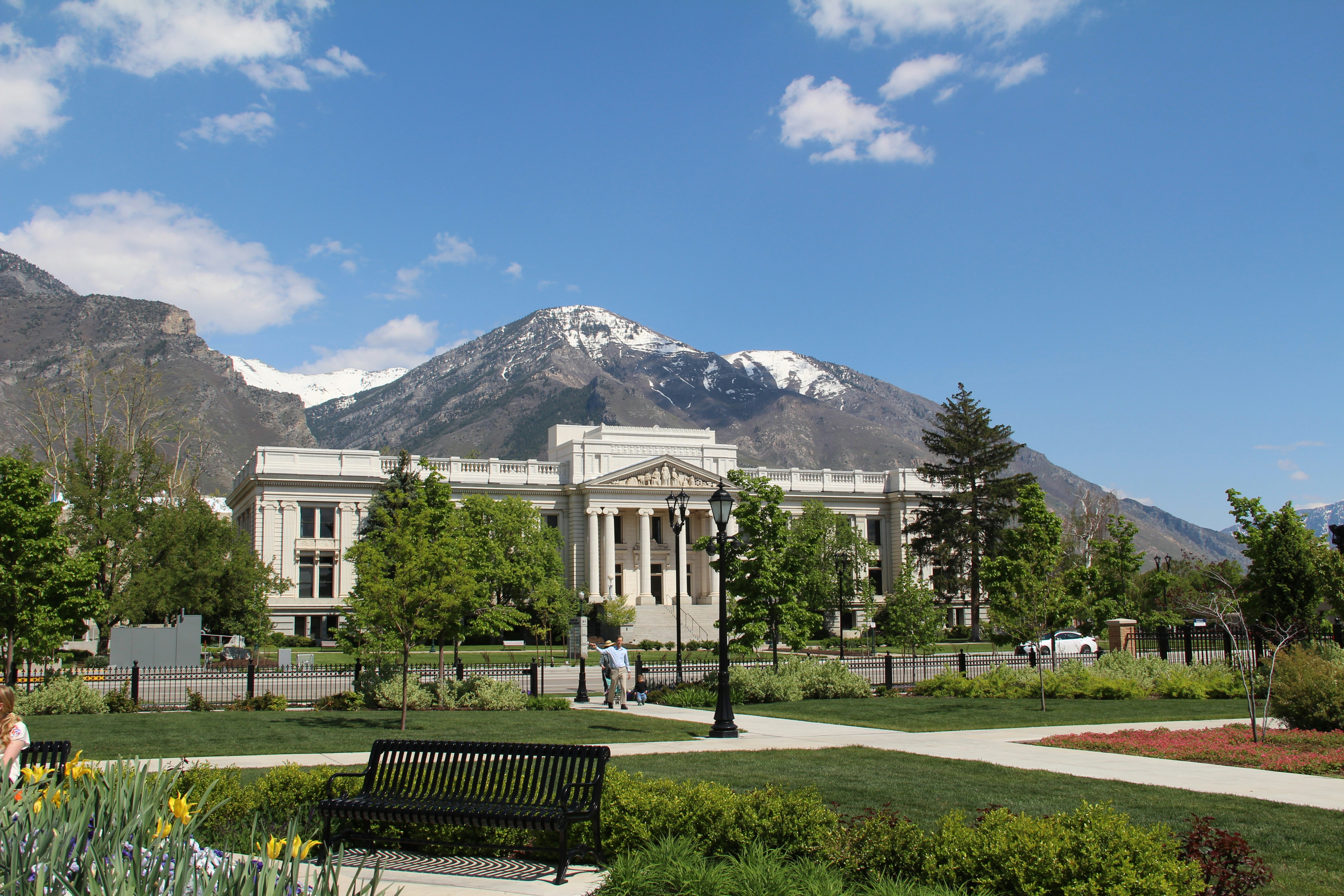 Grand building framed by lush greenery with snow-capped mountains in the background under a clear blue sky.