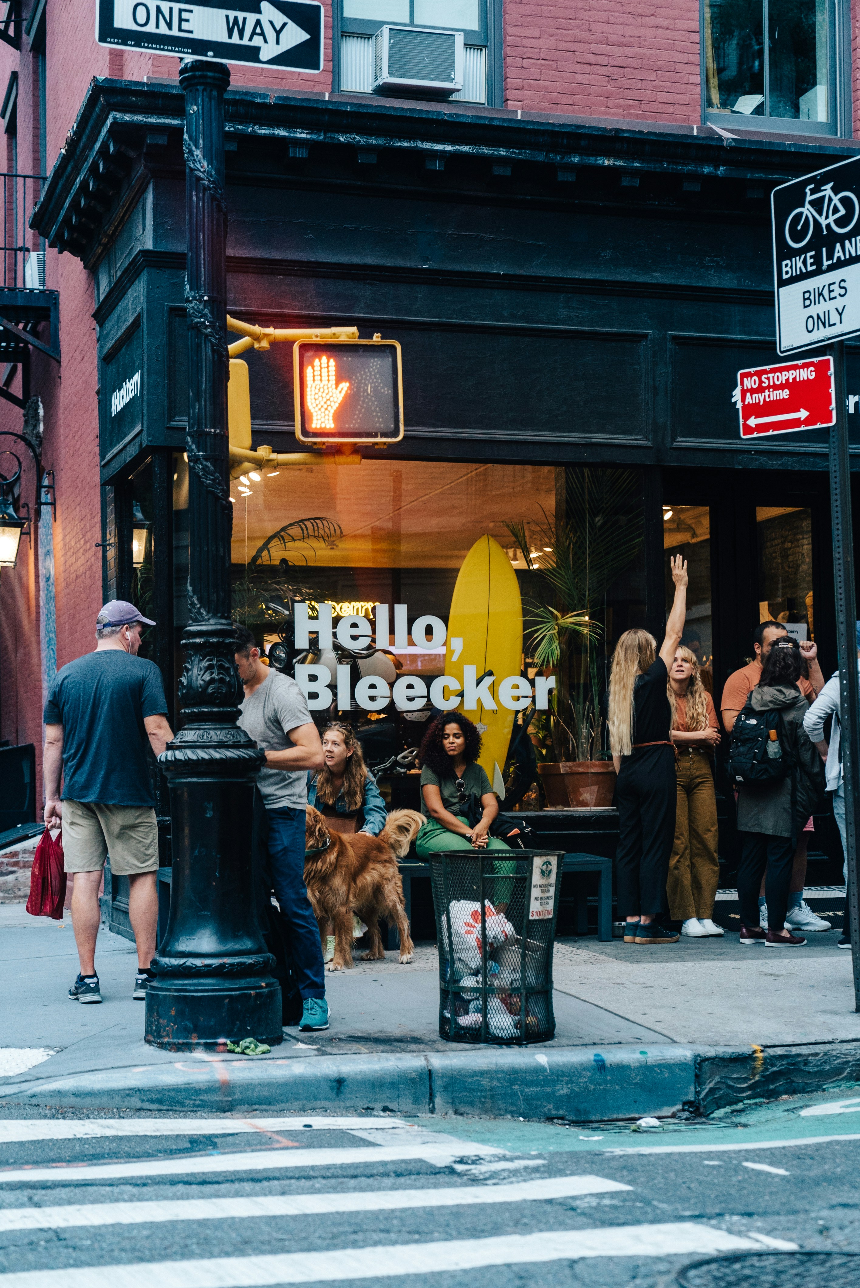 Evening Convergence at Hello, Bleecker: Pedestrians Gather by a Window Sign