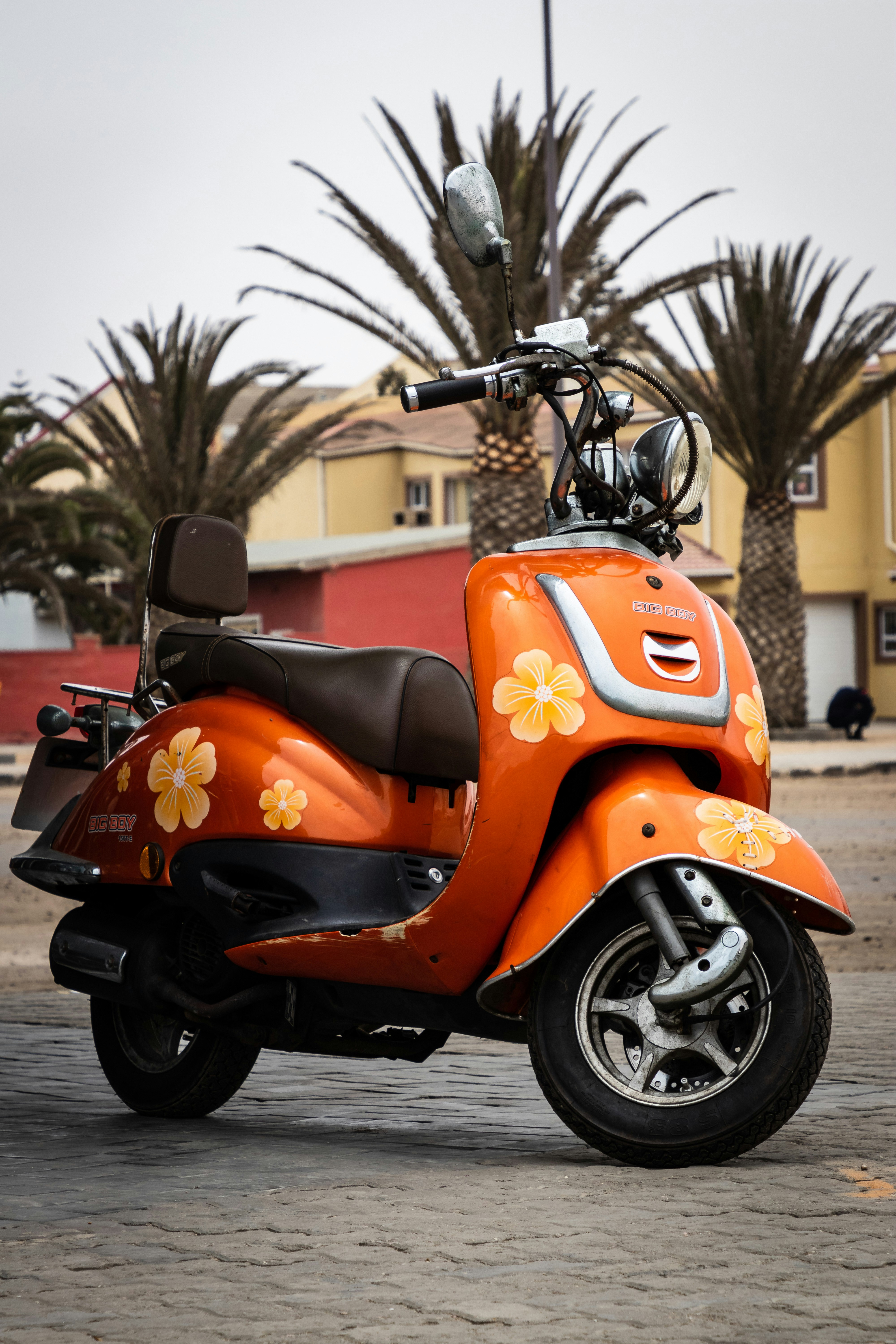 Sunlit Orange Vespa with Hibiscus Decals Stands Out Under Palm Trees