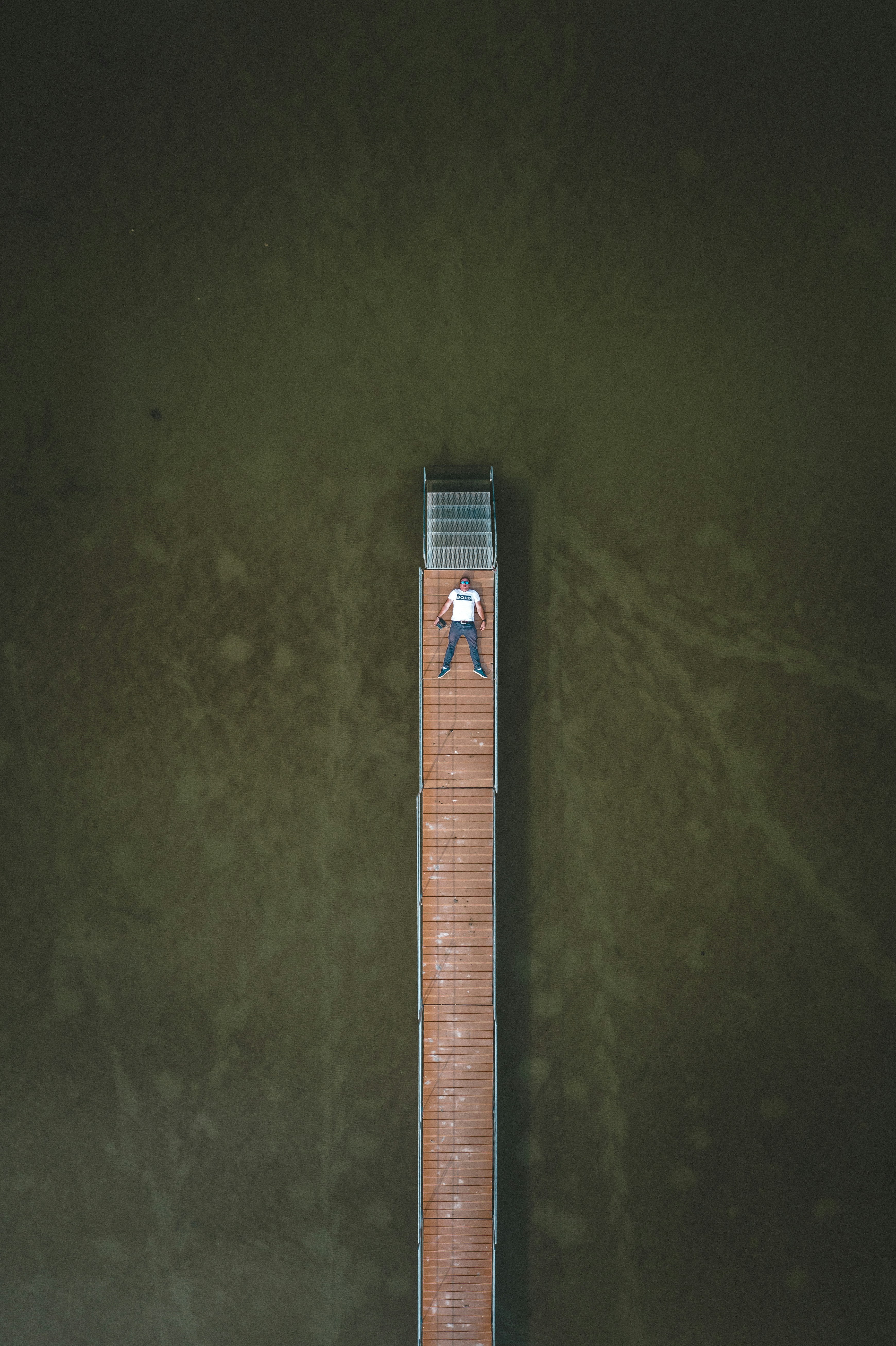 Lone Figure on a Narrow Pier: Stillness Over Murky Green Water
