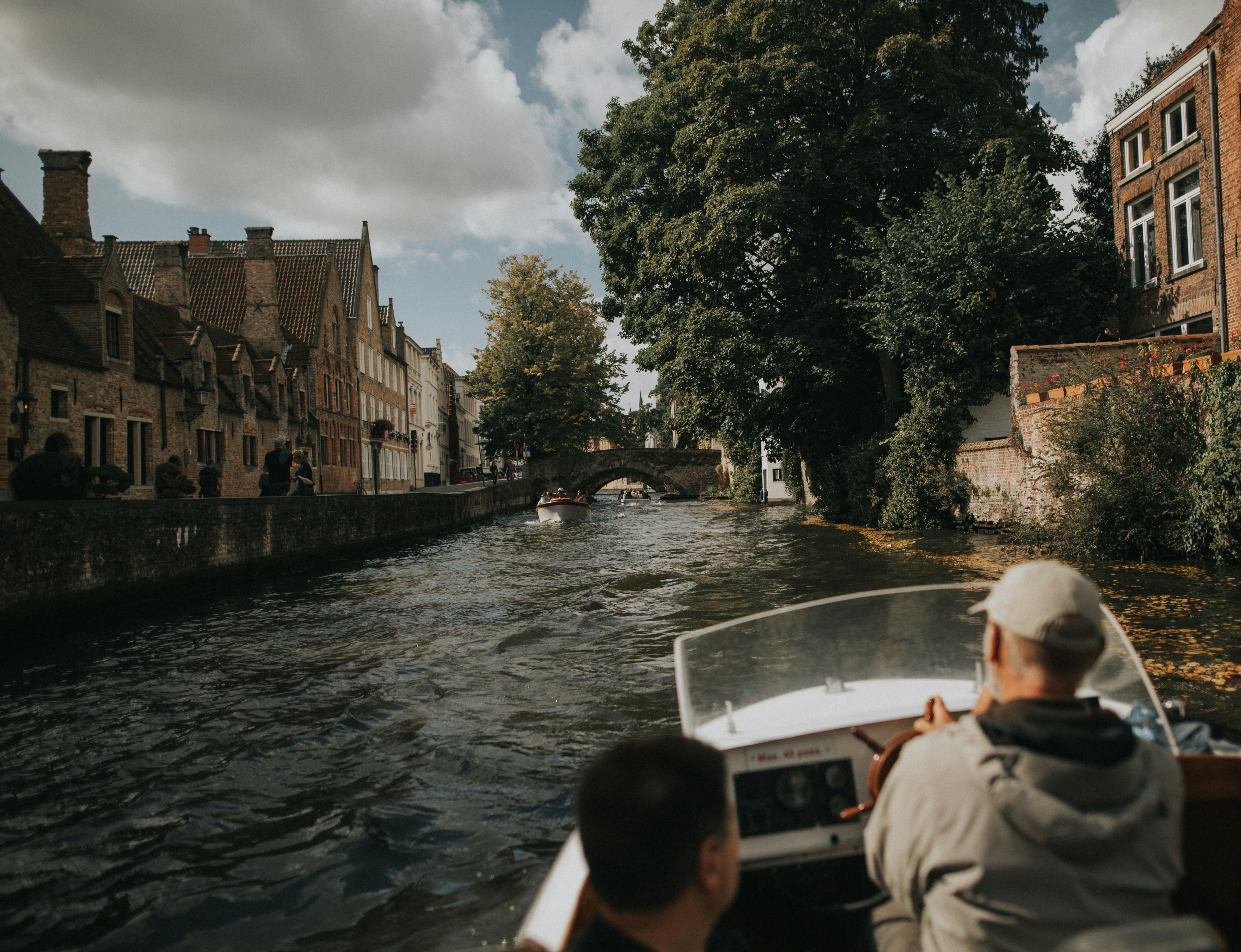 A serene boat ride through the picturesque canals of Bruges, showcasing charming architecture and lush greenery. The scene captures a moment of leisure amidst historical beauty.
