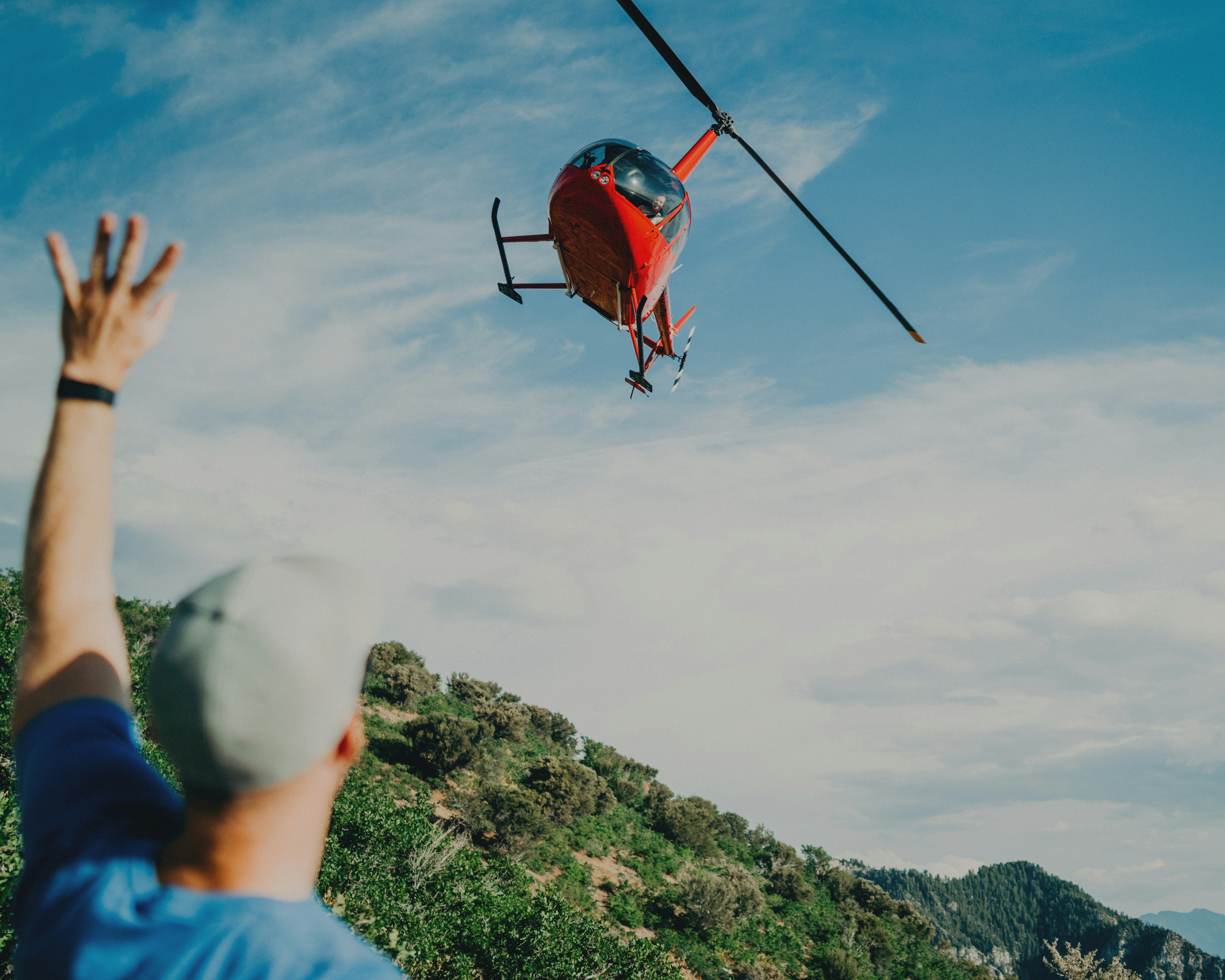 Crimson Rotorcraft Over Ridge: A Helicopter Lift-Off Framed by a Reaching Bystander