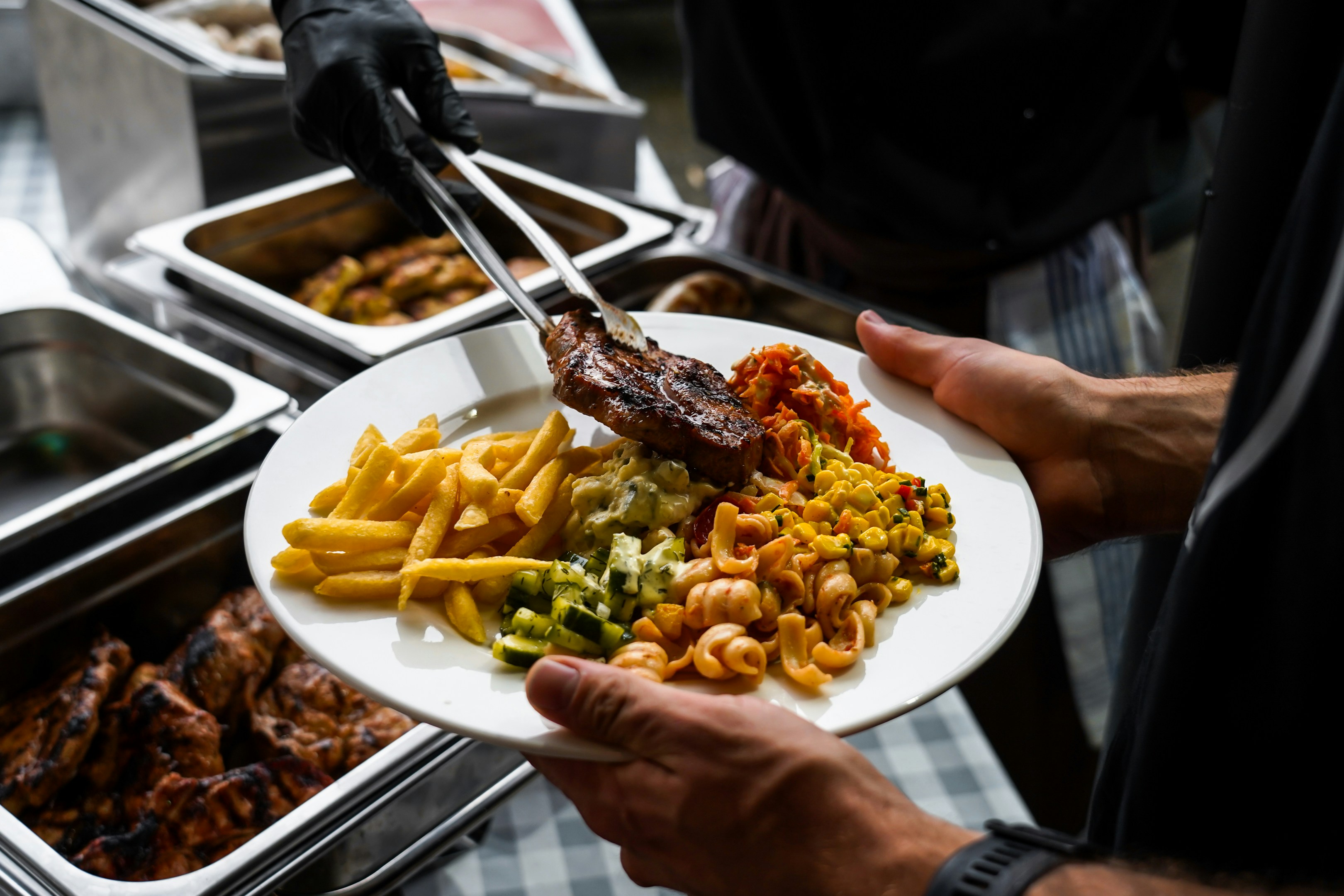 Tongs Lift Roast Over a Buffet Plate of Fries and Pasta