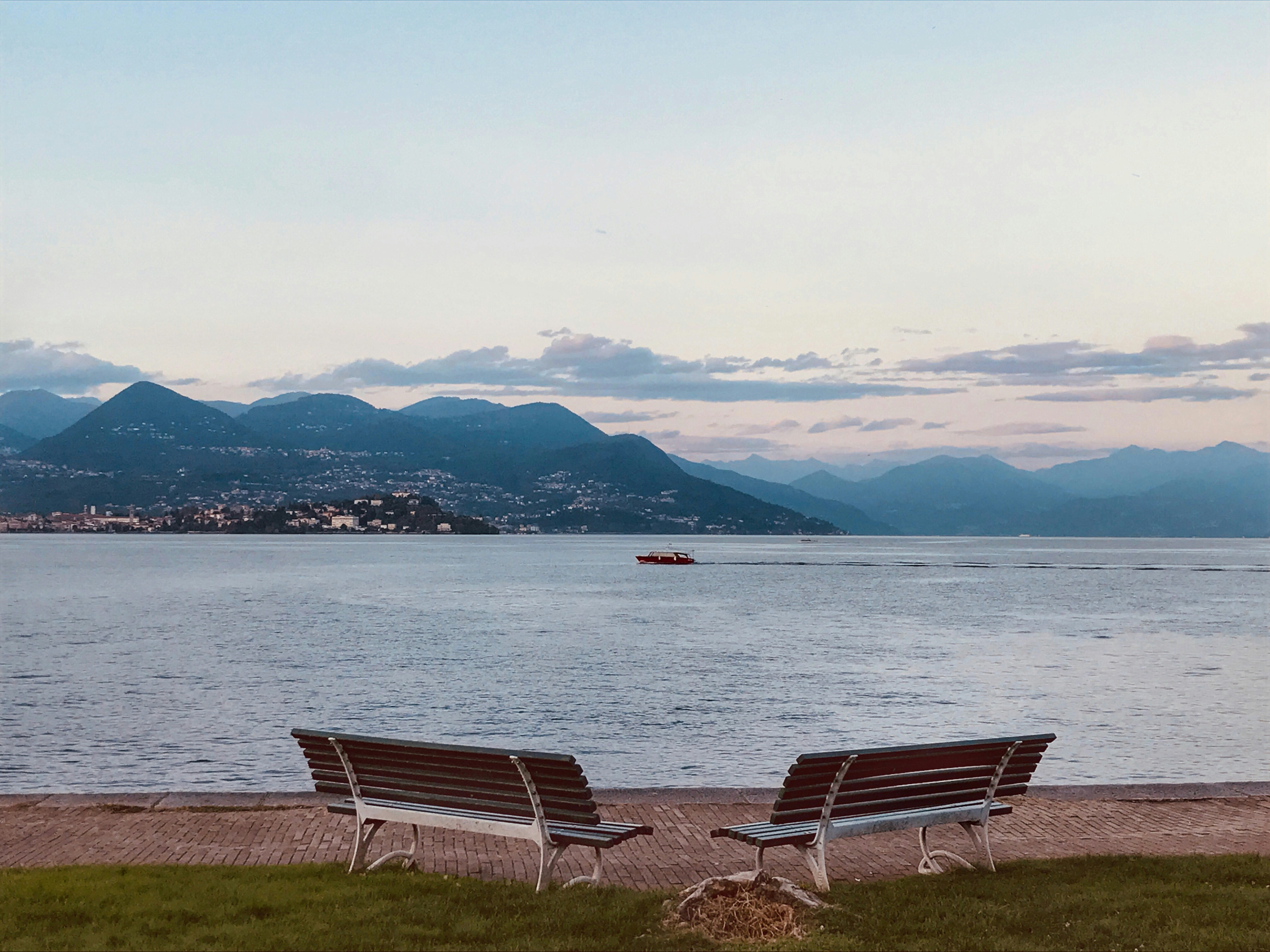 Two empty benches overlook a tranquil lake, framed by distant mountains under a pastel sky.