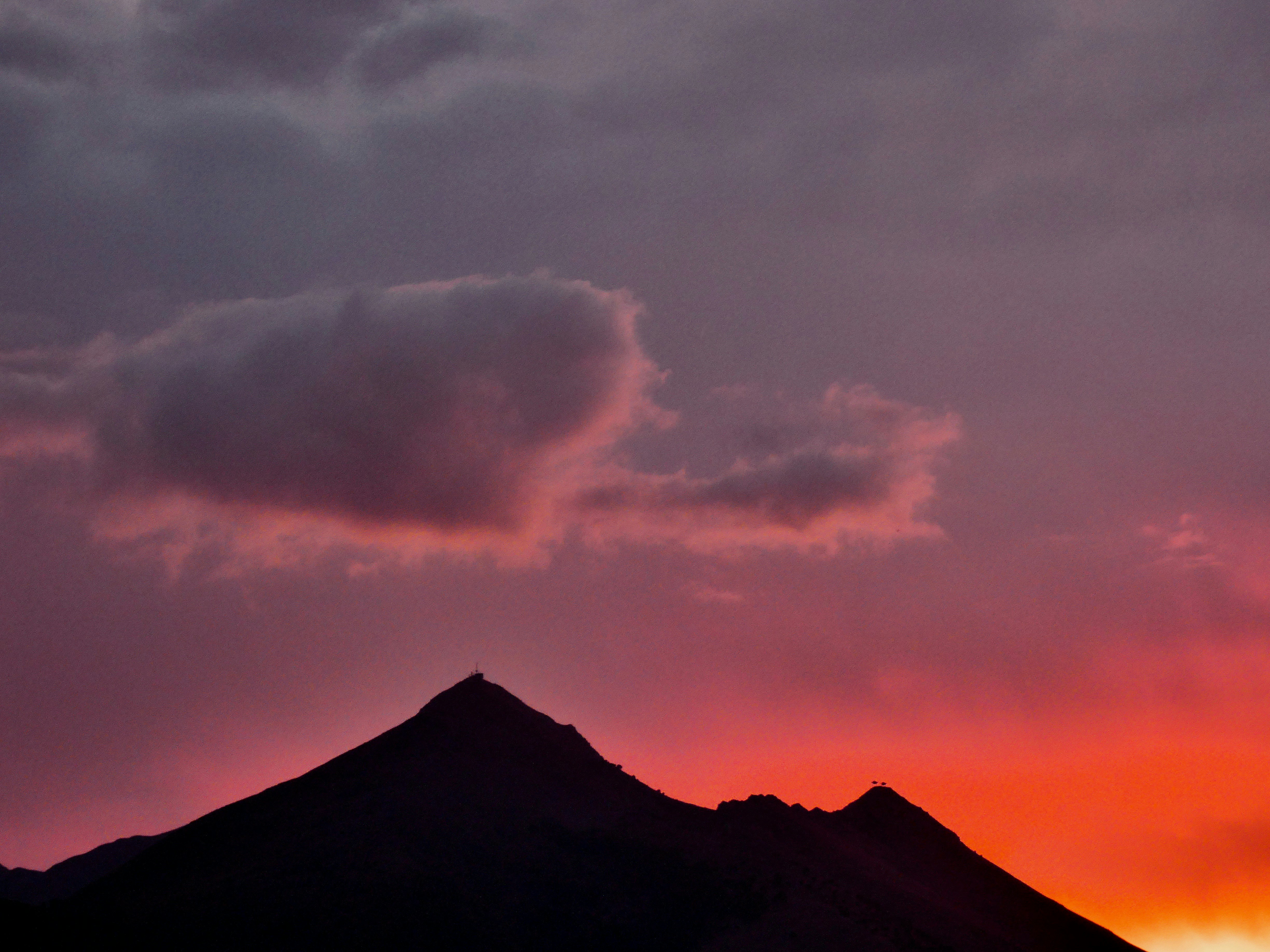 Silhouette of Mount Cuccio against a vibrant sunset sky with dramatic clouds.