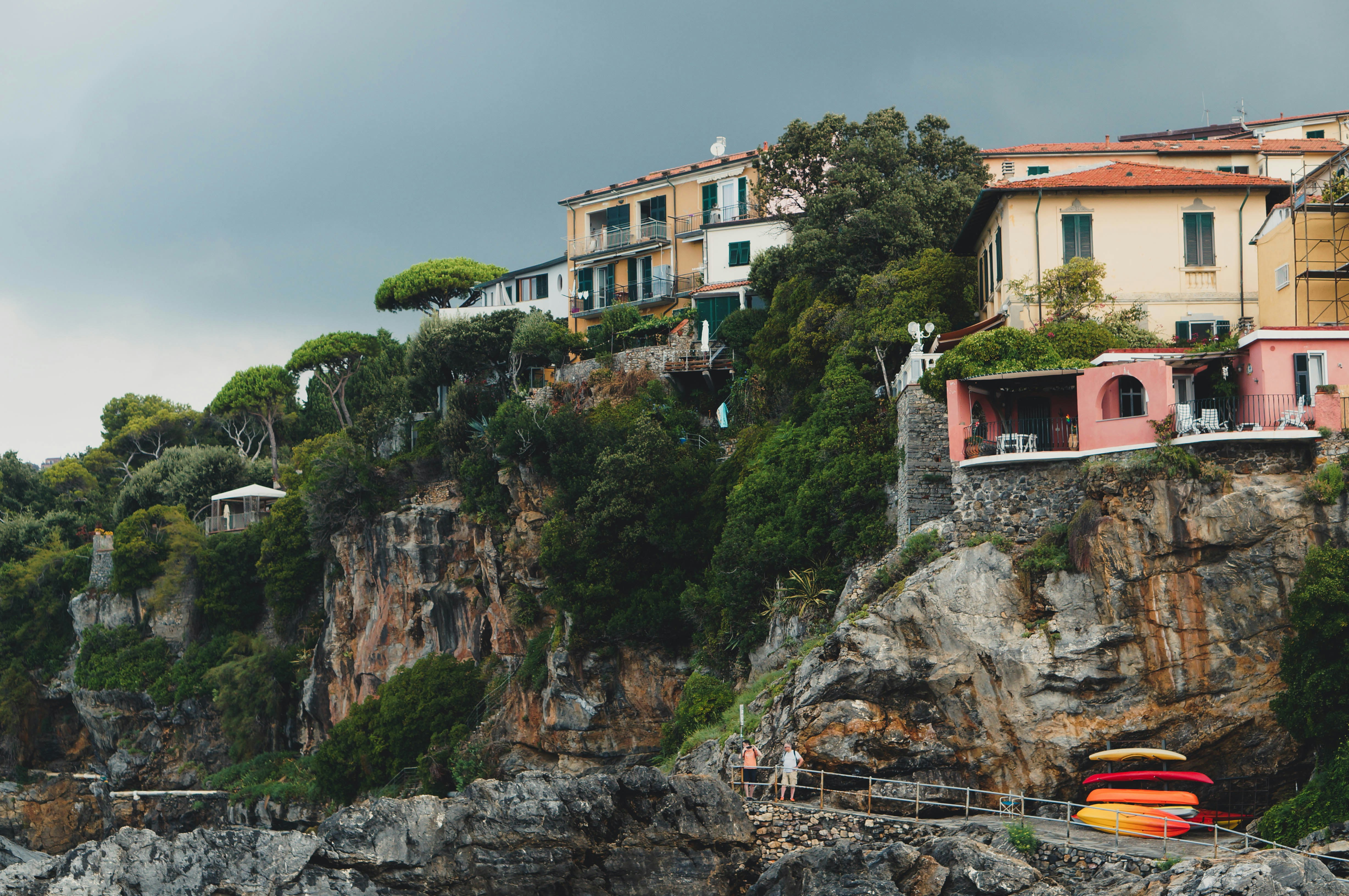 Colorful houses perched on a rocky cliff, surrounded by lush greenery and a serene sea. Kayaks are lined up along the shore, inviting adventure.