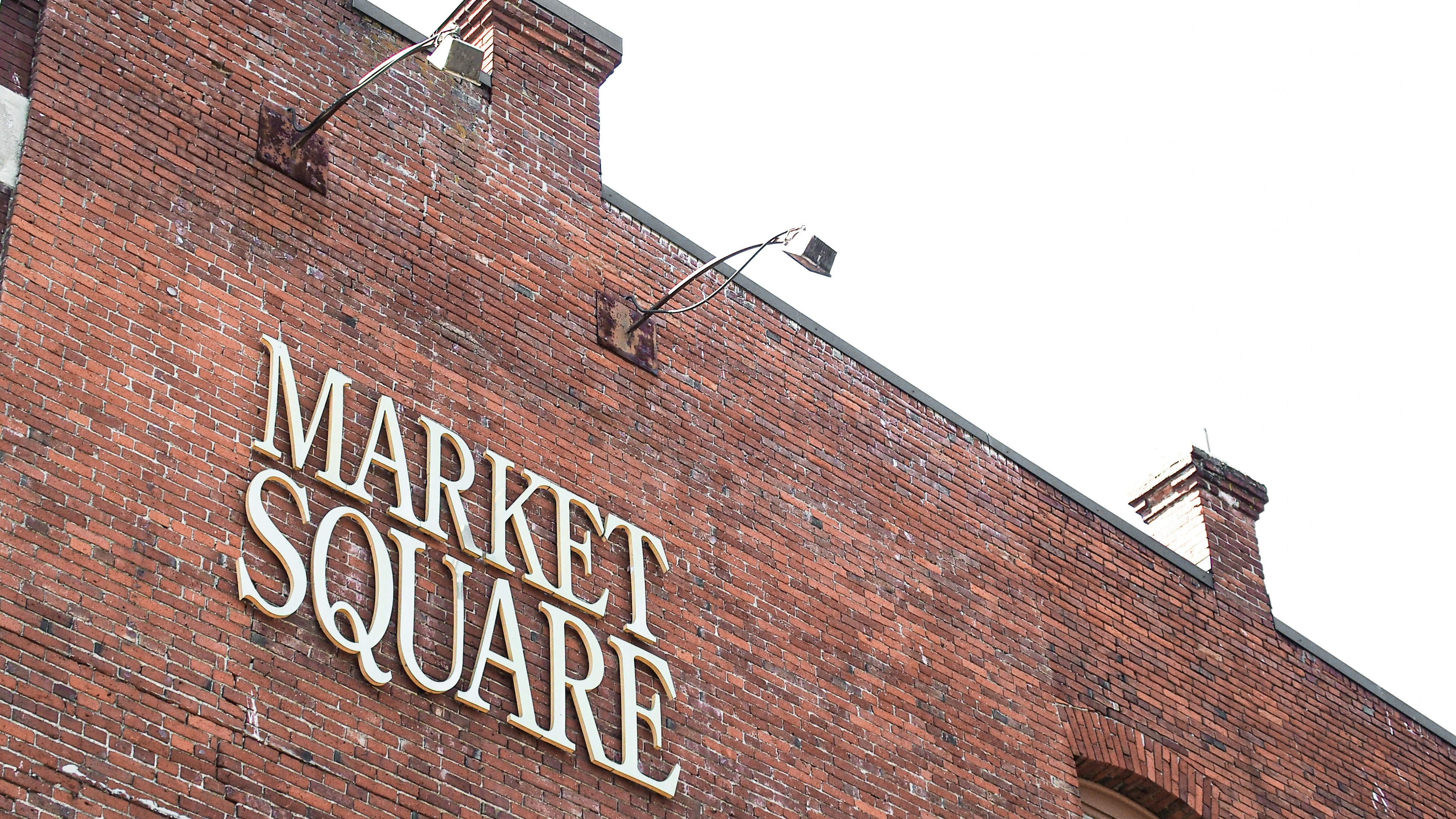 Brick building facade with 'Market Square' sign against a bright sky.