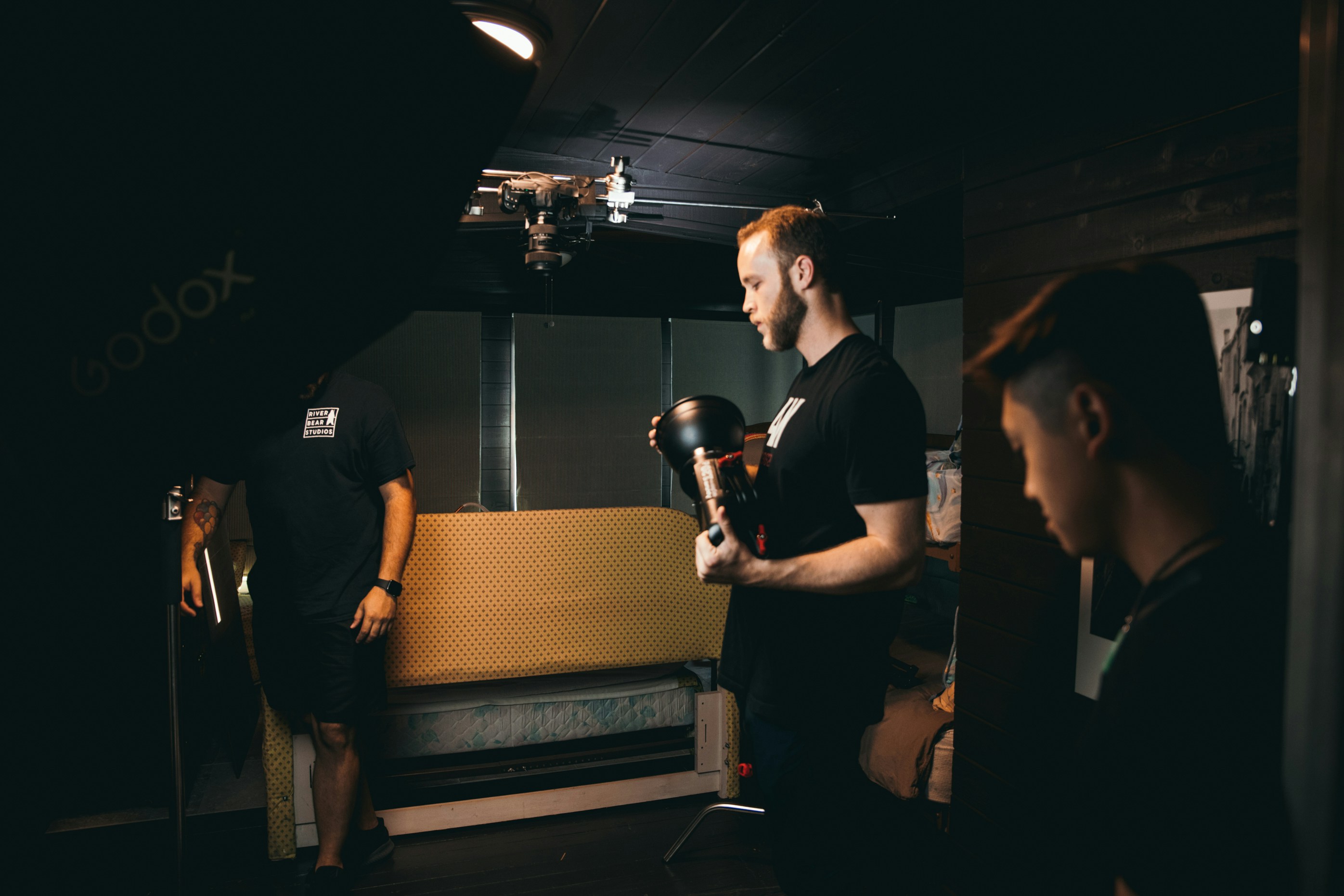 Two individuals engaged in a photography setup, with a softbox illuminating a cozy indoor space featuring a distinctive couch.